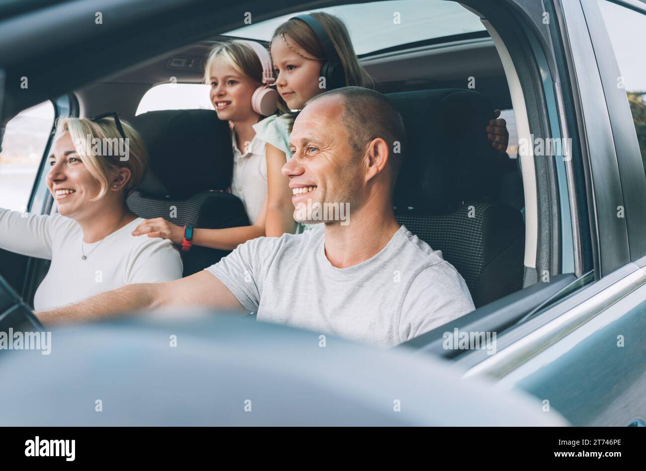 Happy young couple with two daughters inside the modern car with panoramic roof during auto trop ...