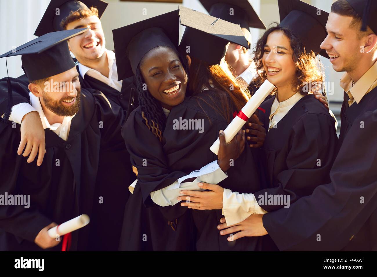 Smiling diverse graduates hugging each other holding diplomas and ...