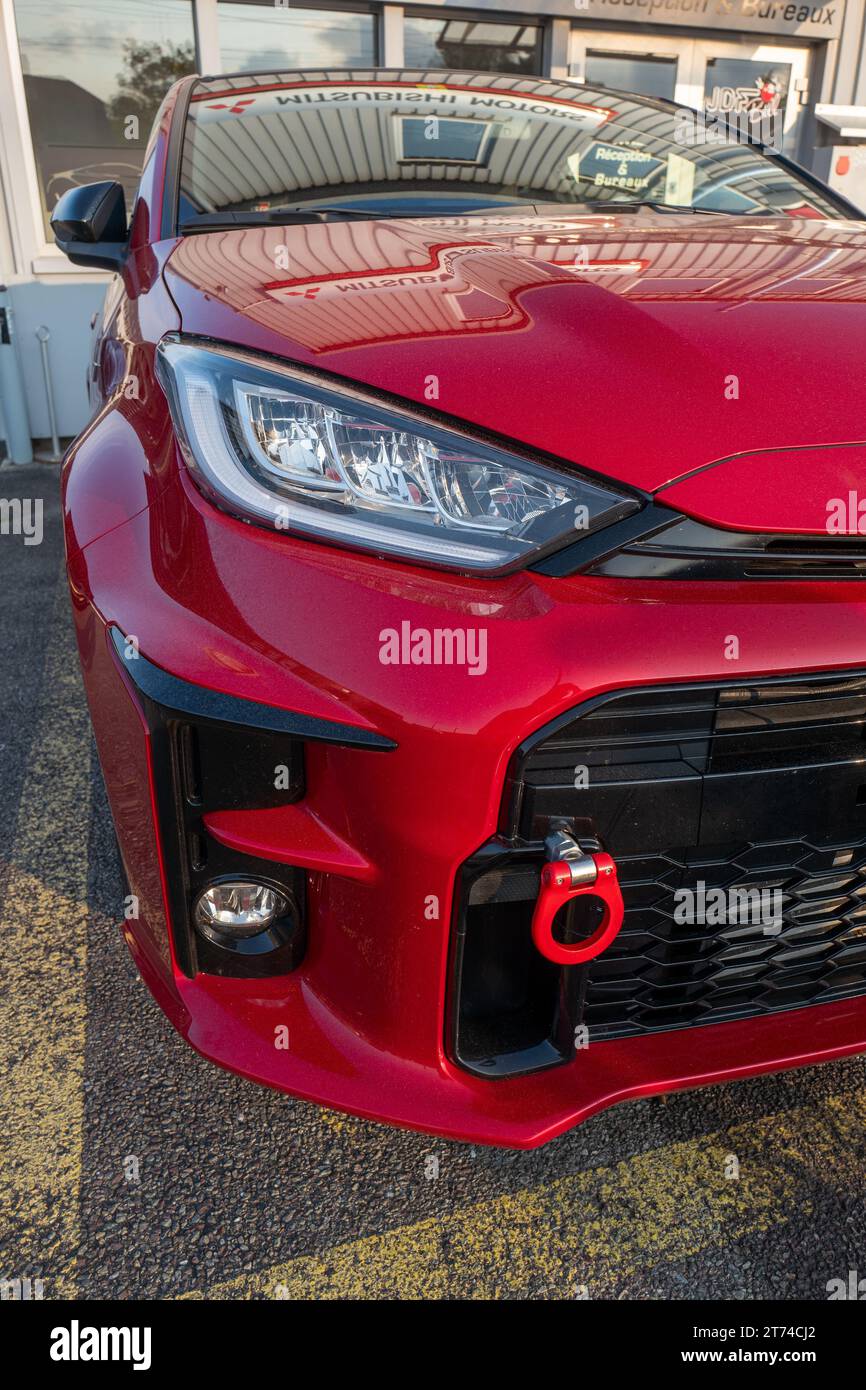 A vibrant red car is featured from the front, with its headlights ...