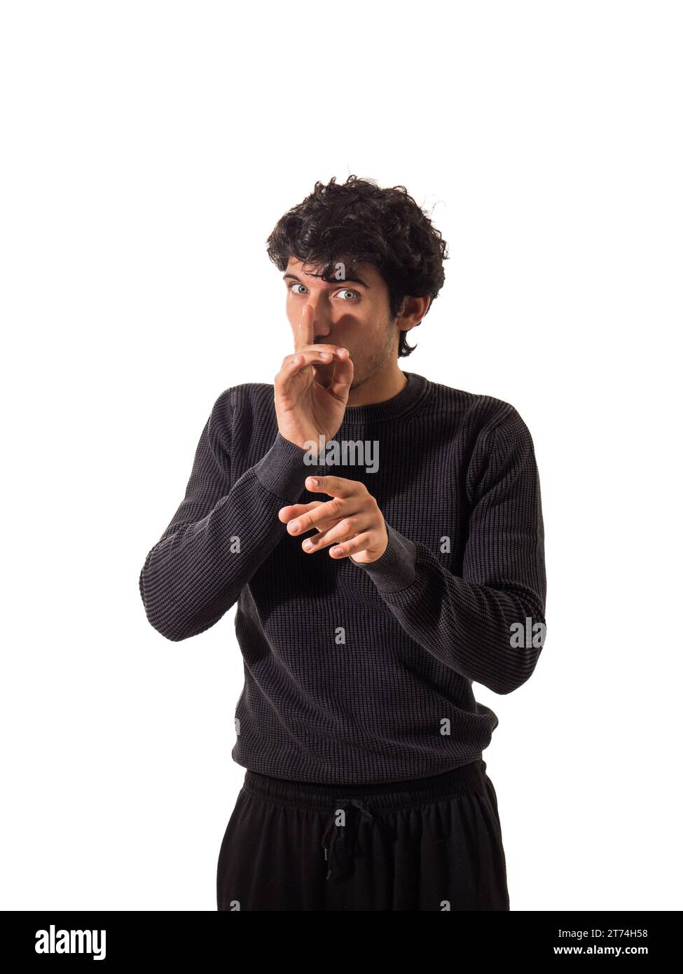 Young man doing hush sign with finger over his mouth, looking at camera ...