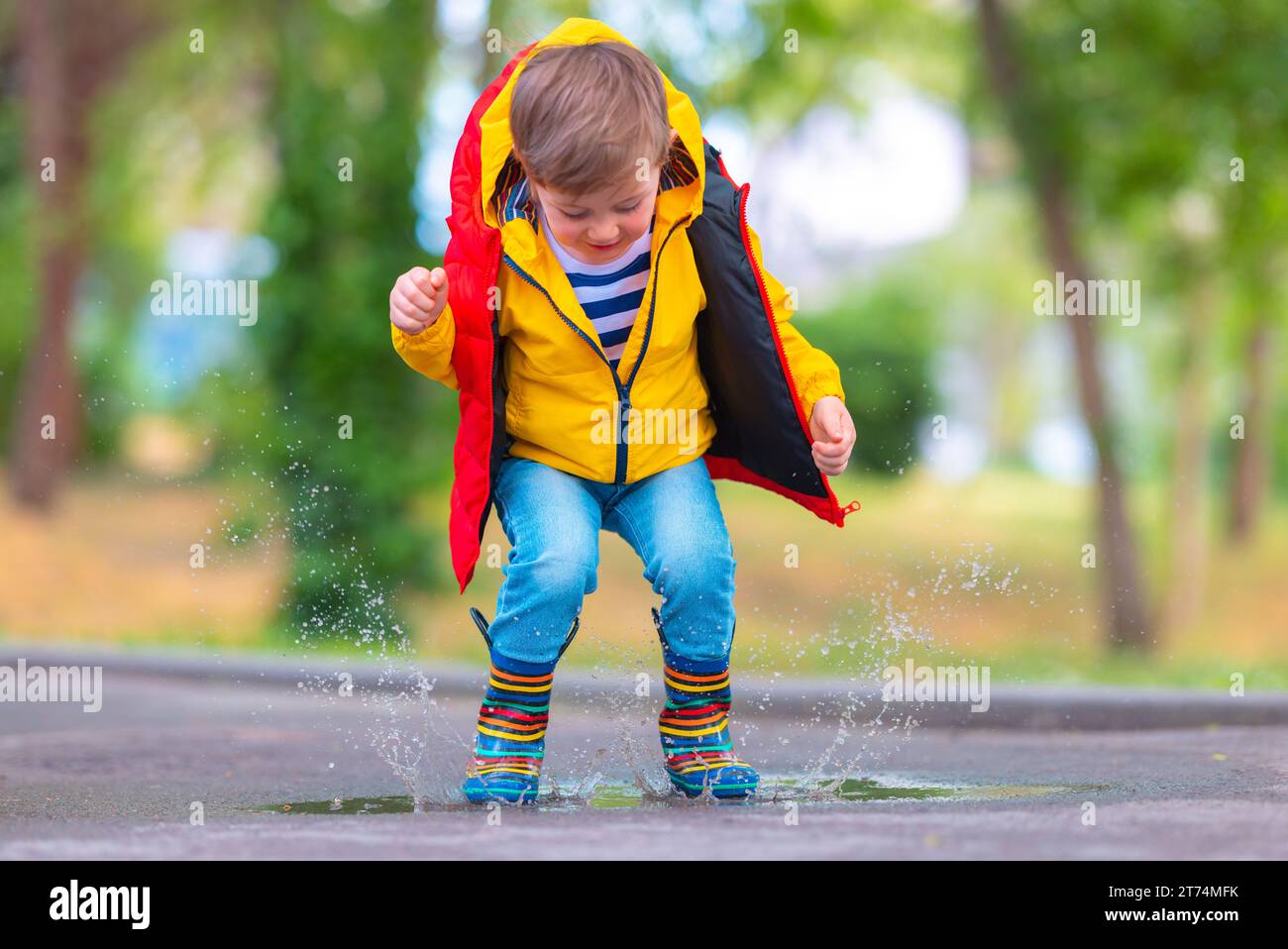 Happy toddler boy with umbrella and color rubber boots jump on a rainy ...