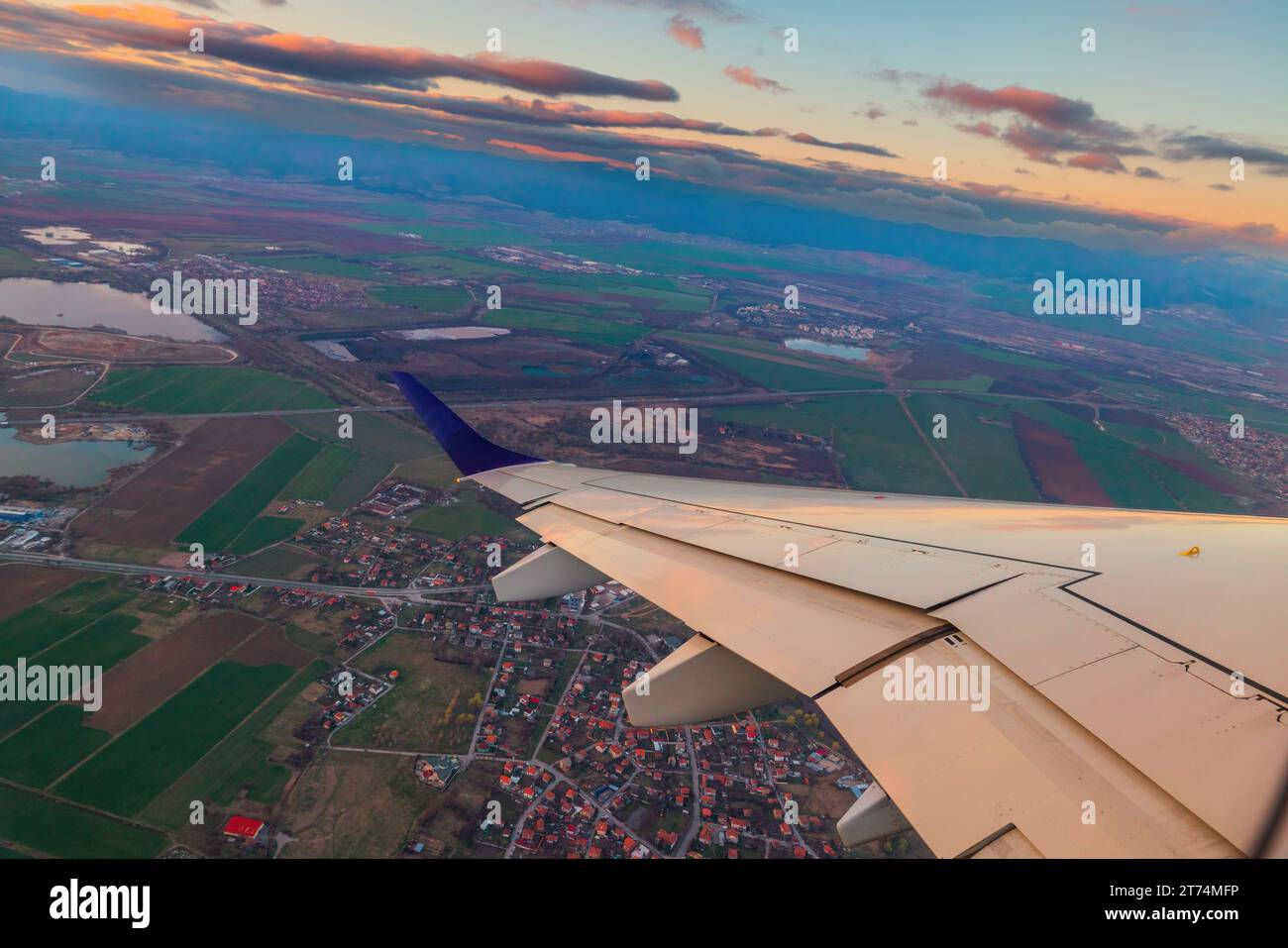 Airplane flight in sunset sky over city and wing of plane. View from ...