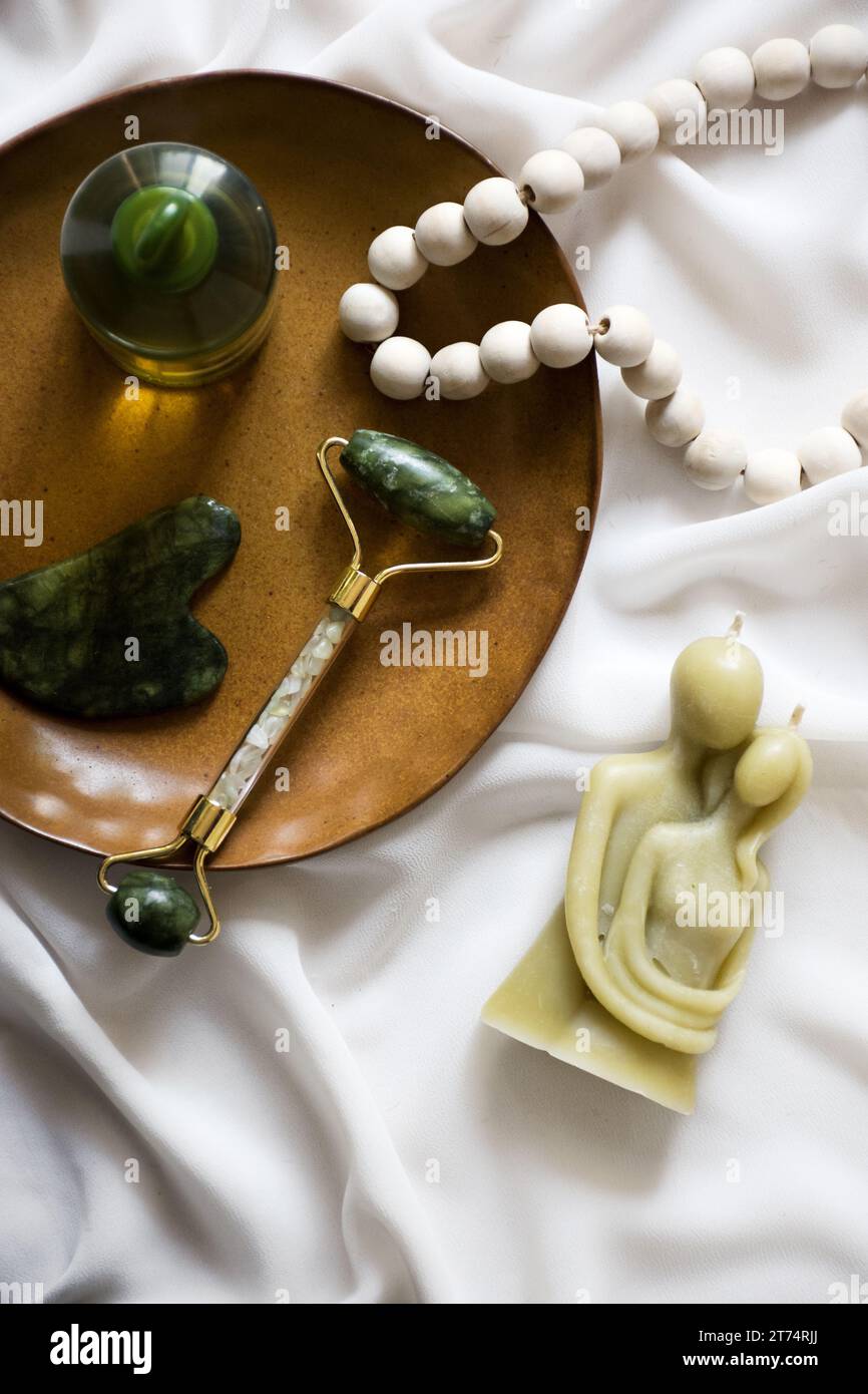 A pearl necklace, a green gua sha laying on top of white clean sheets ...