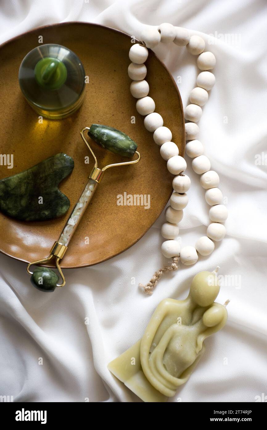 A pearl necklace, a green gua sha laying on top of white clean sheets ...