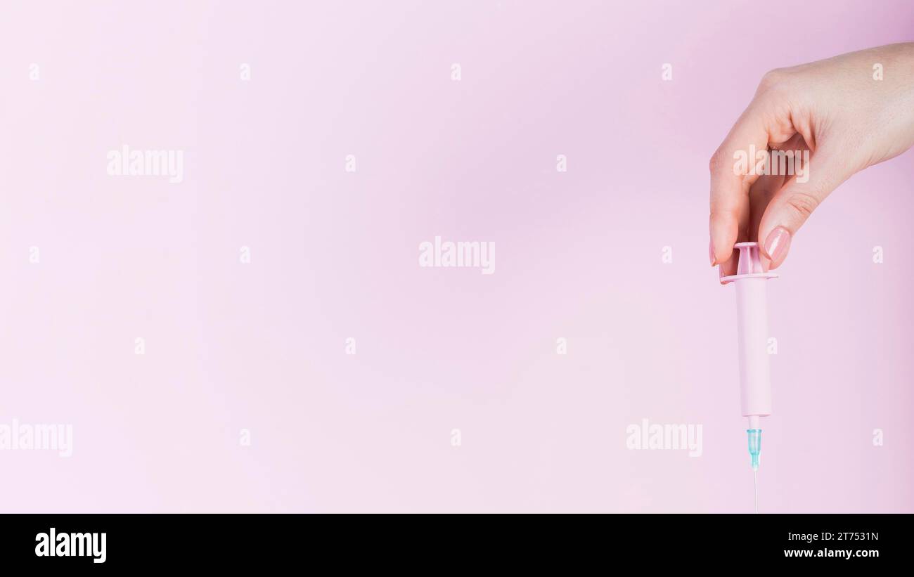 Human hand holding plastic syringe pink backdrop Stock Photo - Alamy