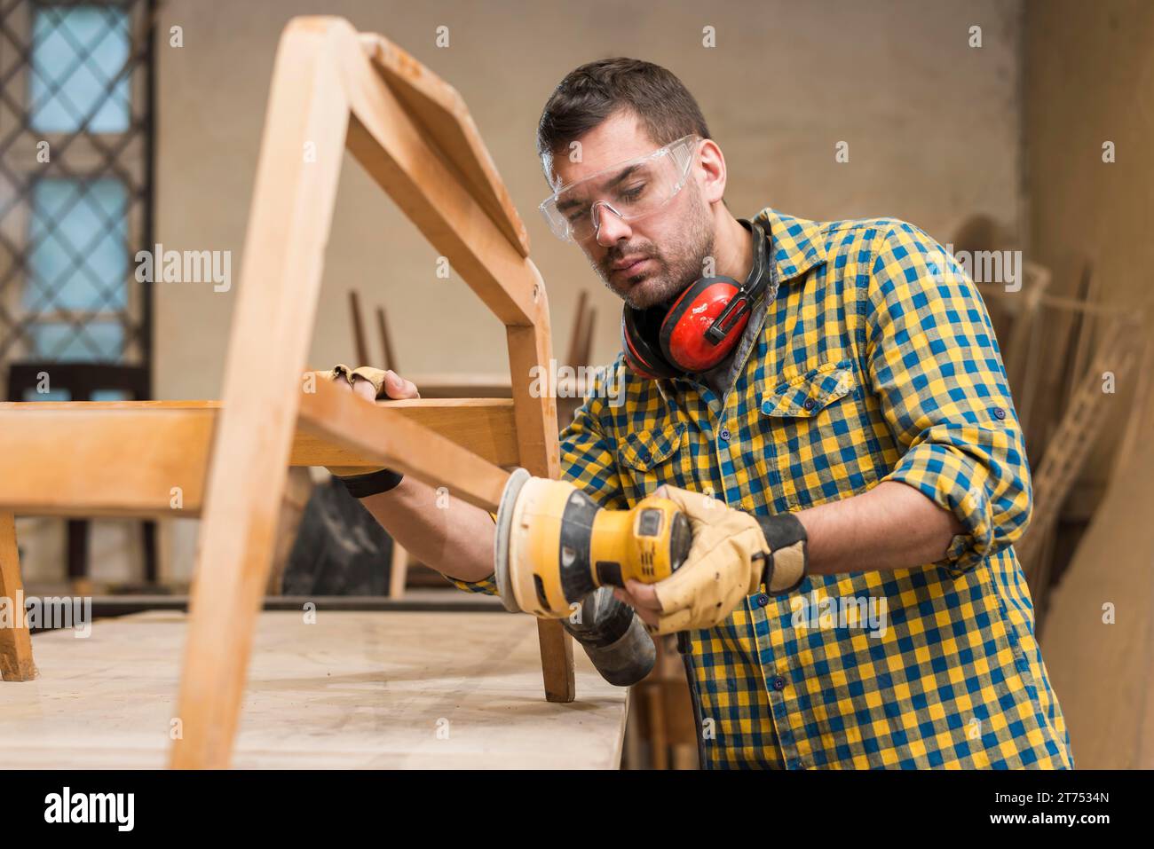 Male carpenter wearing safety glasses using sander furniture workshop ...