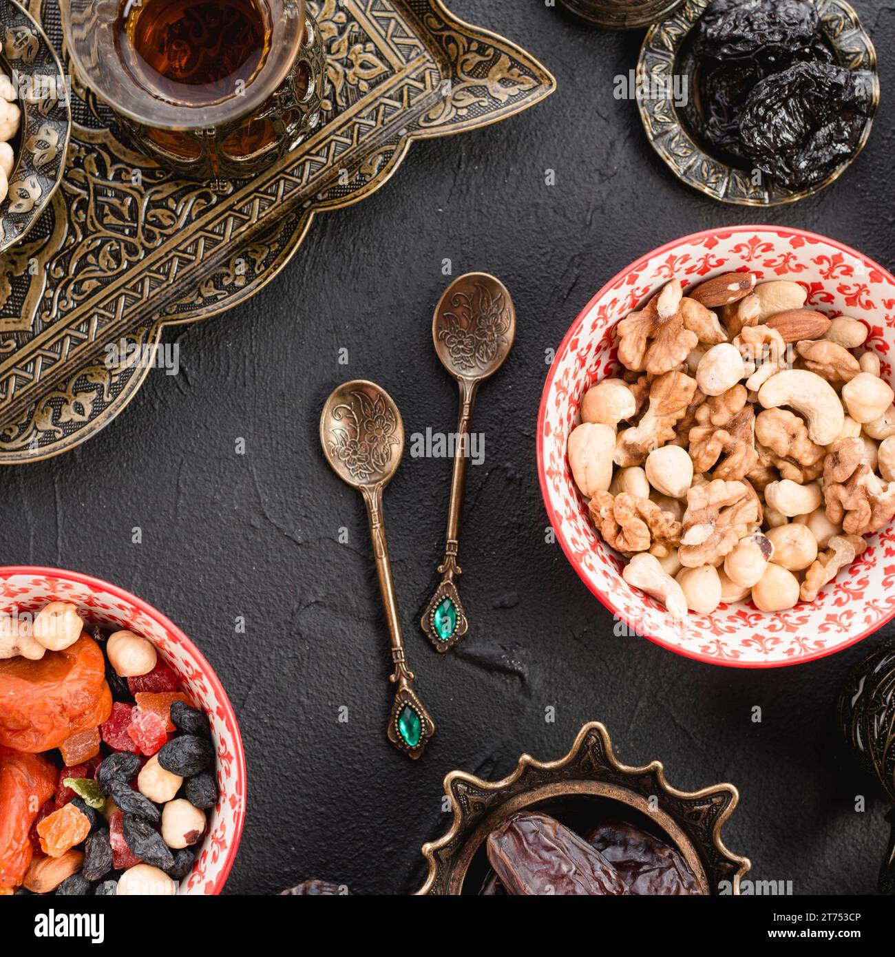 Mixed nuts tea dried fruits metallic spoons black concrete backdrop ...