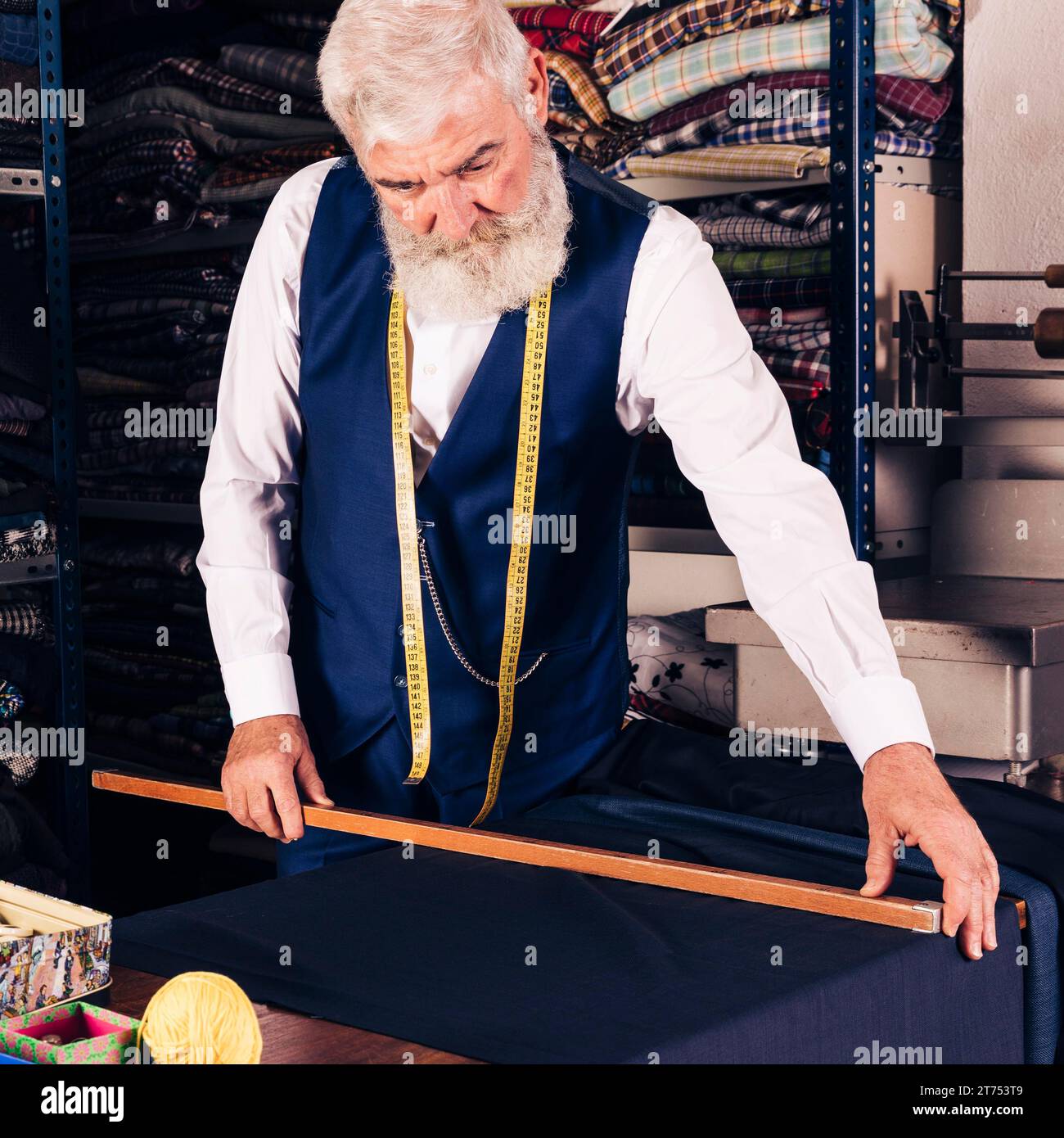 Portrait senior male fashion designer measuring fabric with wooden ...