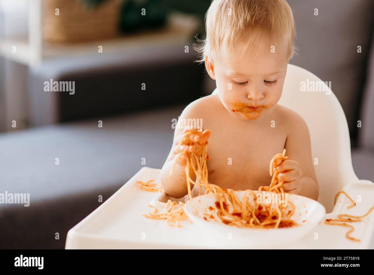 Baby boy eating pasta his highchair making mess Stock Photo - Alamy