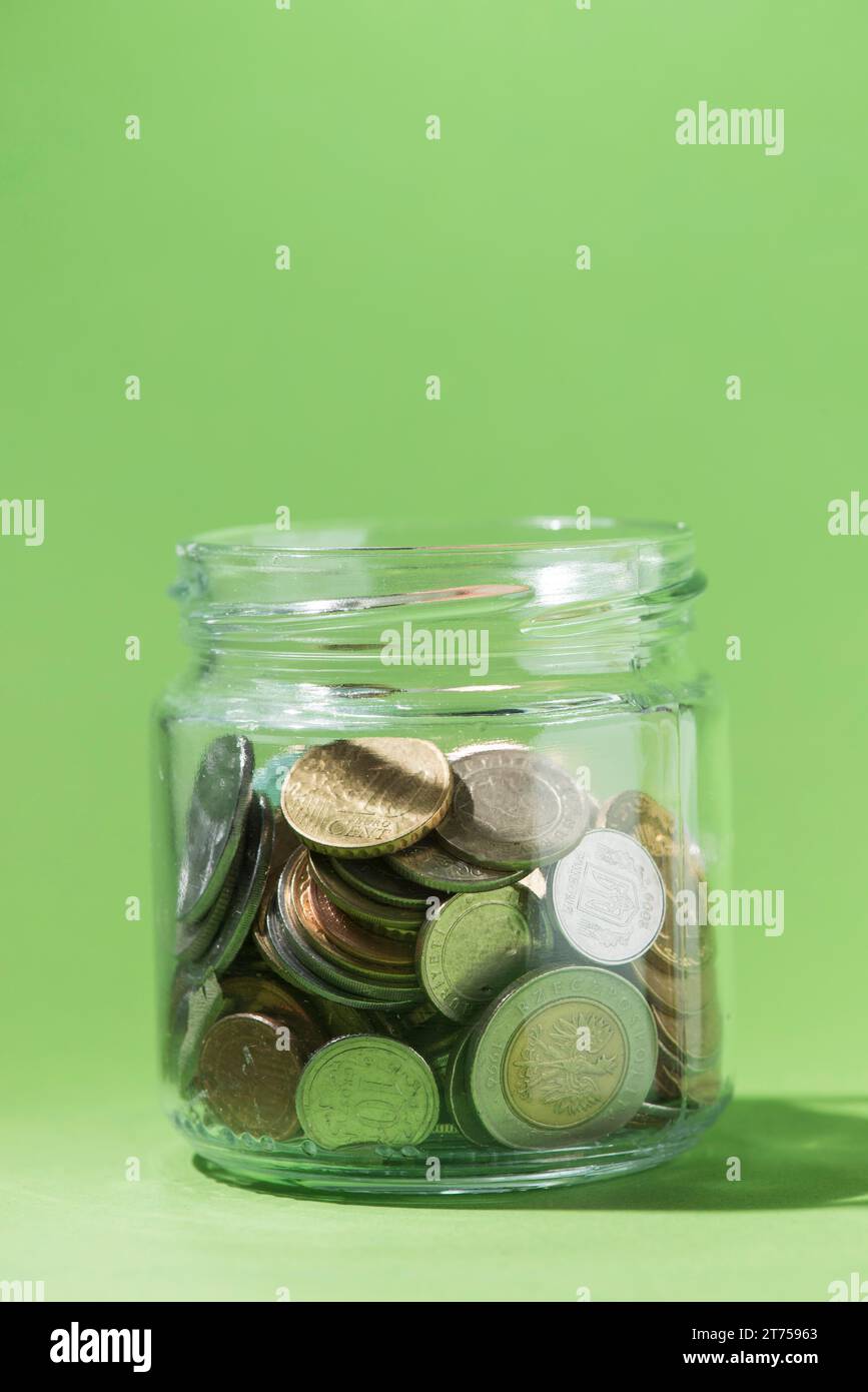 Close up coins inside glass container green background Stock Photo - Alamy