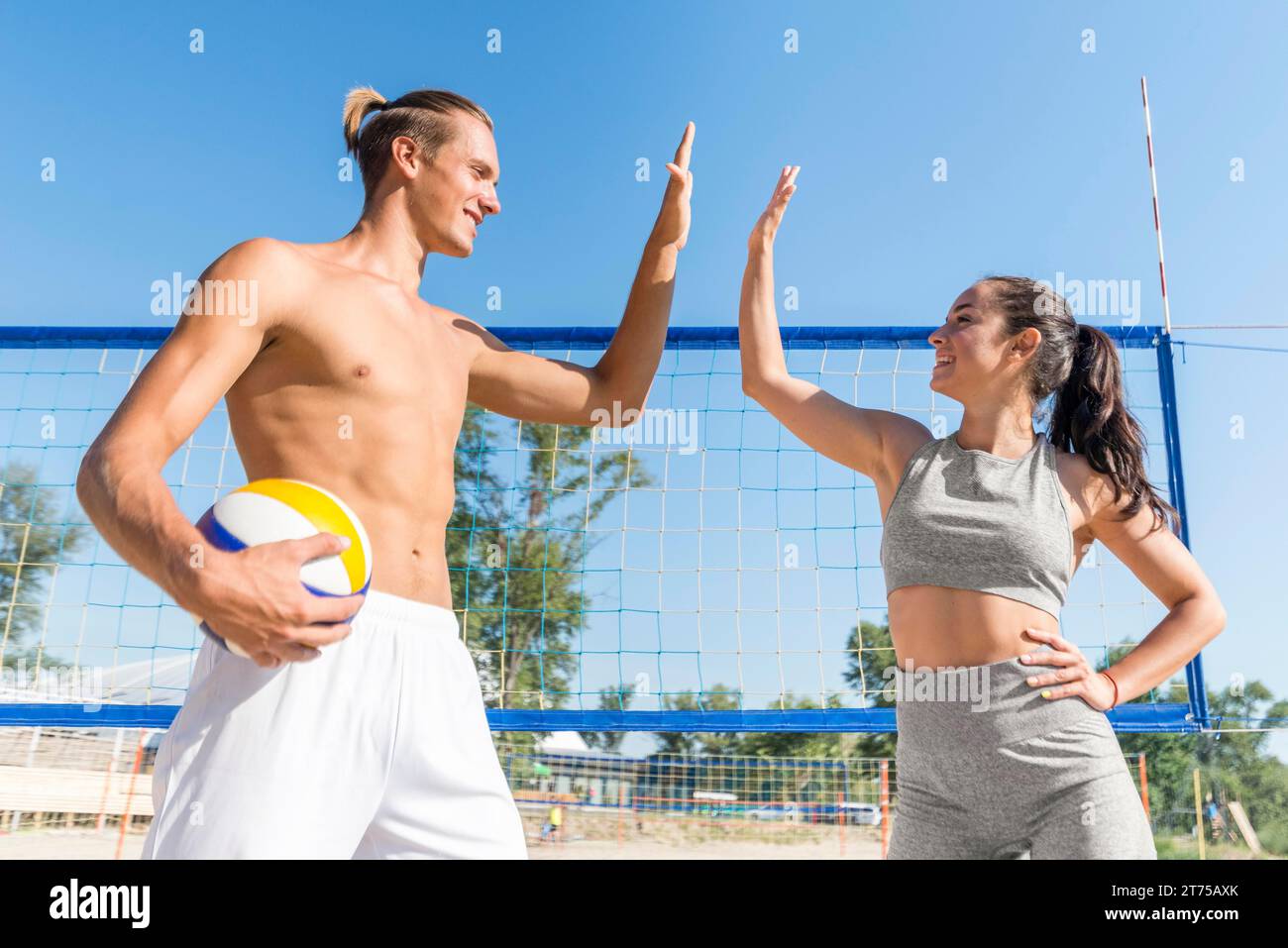 Side view man woman high fiving each other while playing volleyball ...