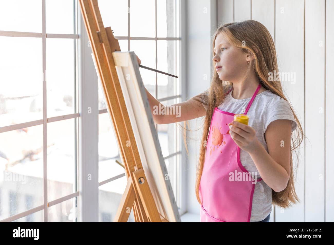 Side view girl holding yellow paint bottle hand painting easel with ...