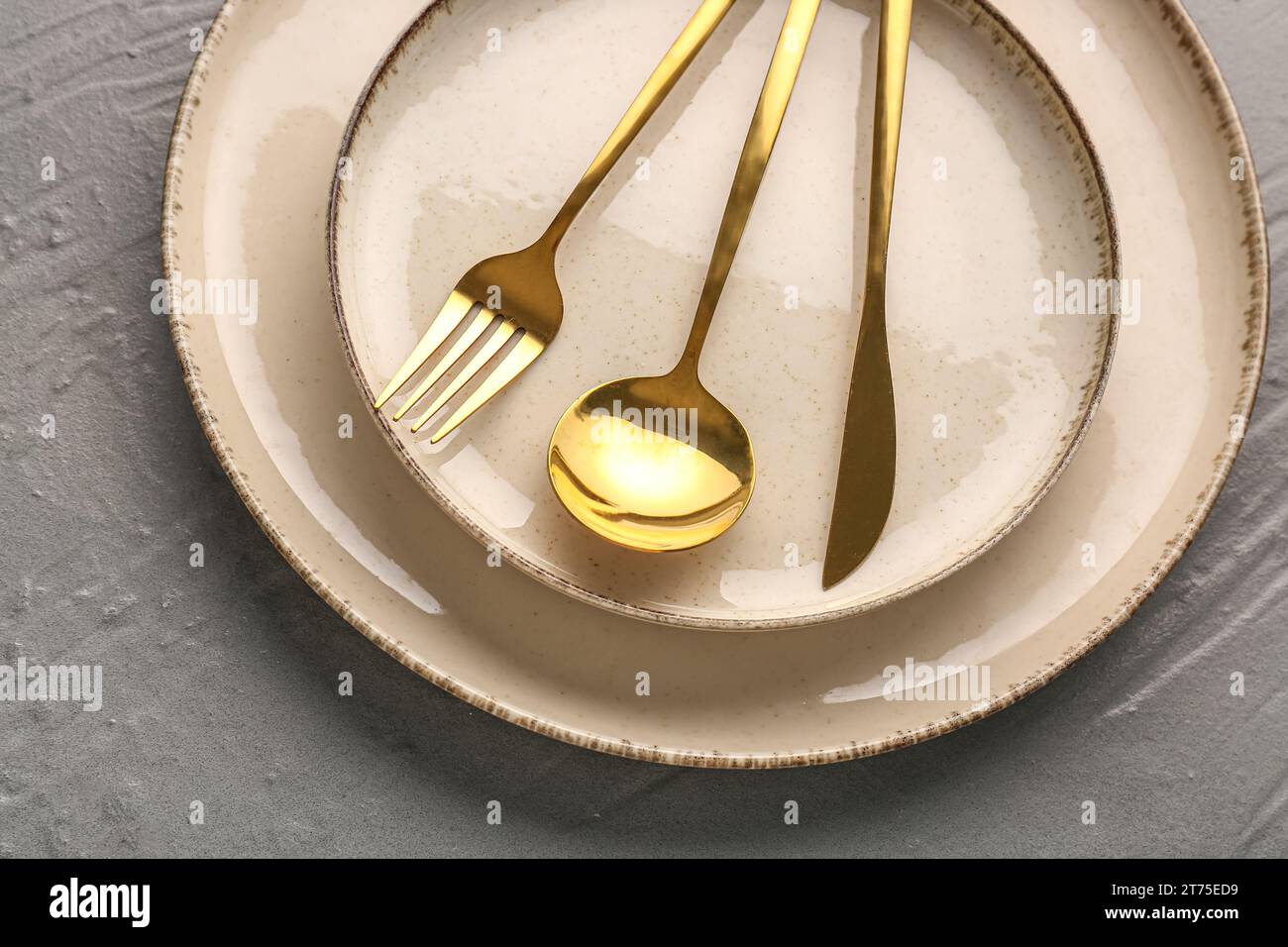 Golden set of cutlery with beige plates on grey background Stock Photo ...