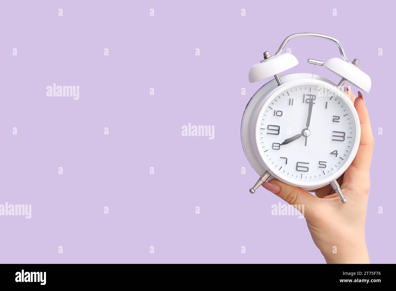 Female hand holding alarm clock on lilac background Stock Photo - Alamy