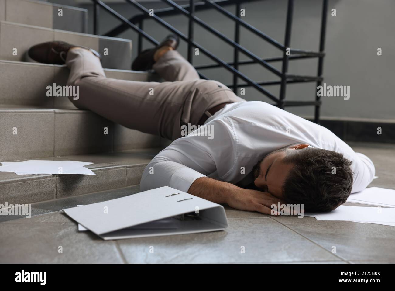 Unconscious man with scattered folder and papers lying on floor after ...