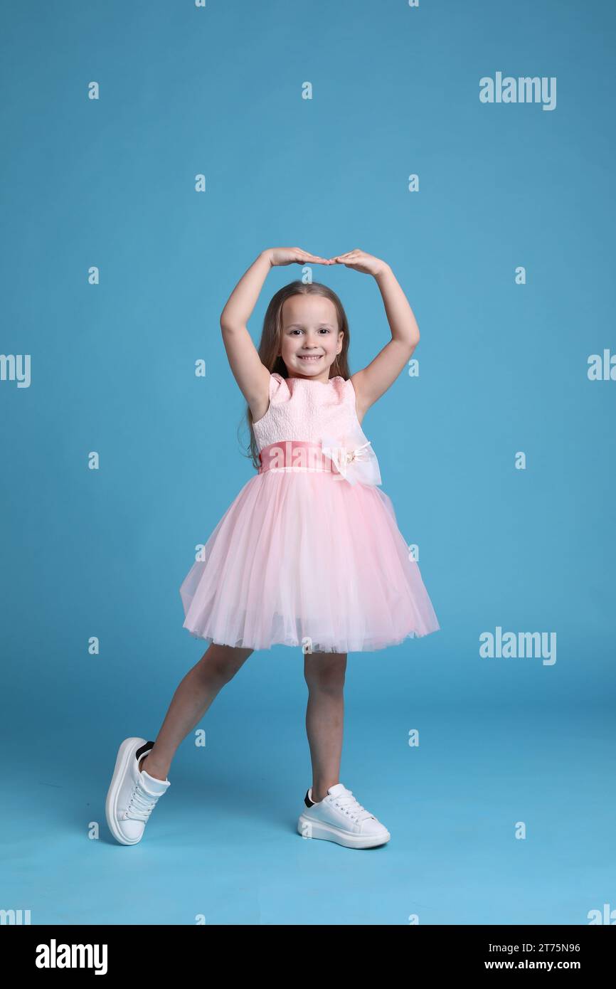 Cute little girl in beautiful dress dancing on light blue background ...