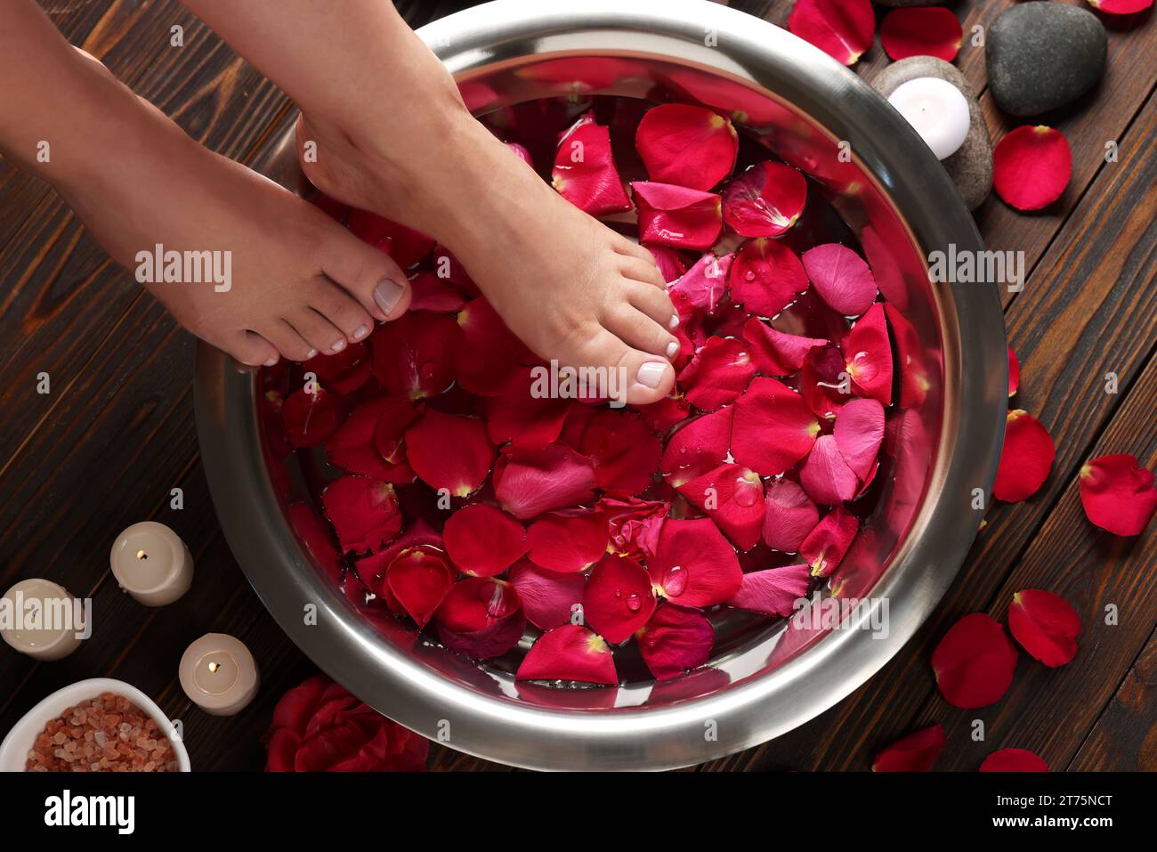 Woman soaking her feet in bowl with water and red rose petals on wooden ...