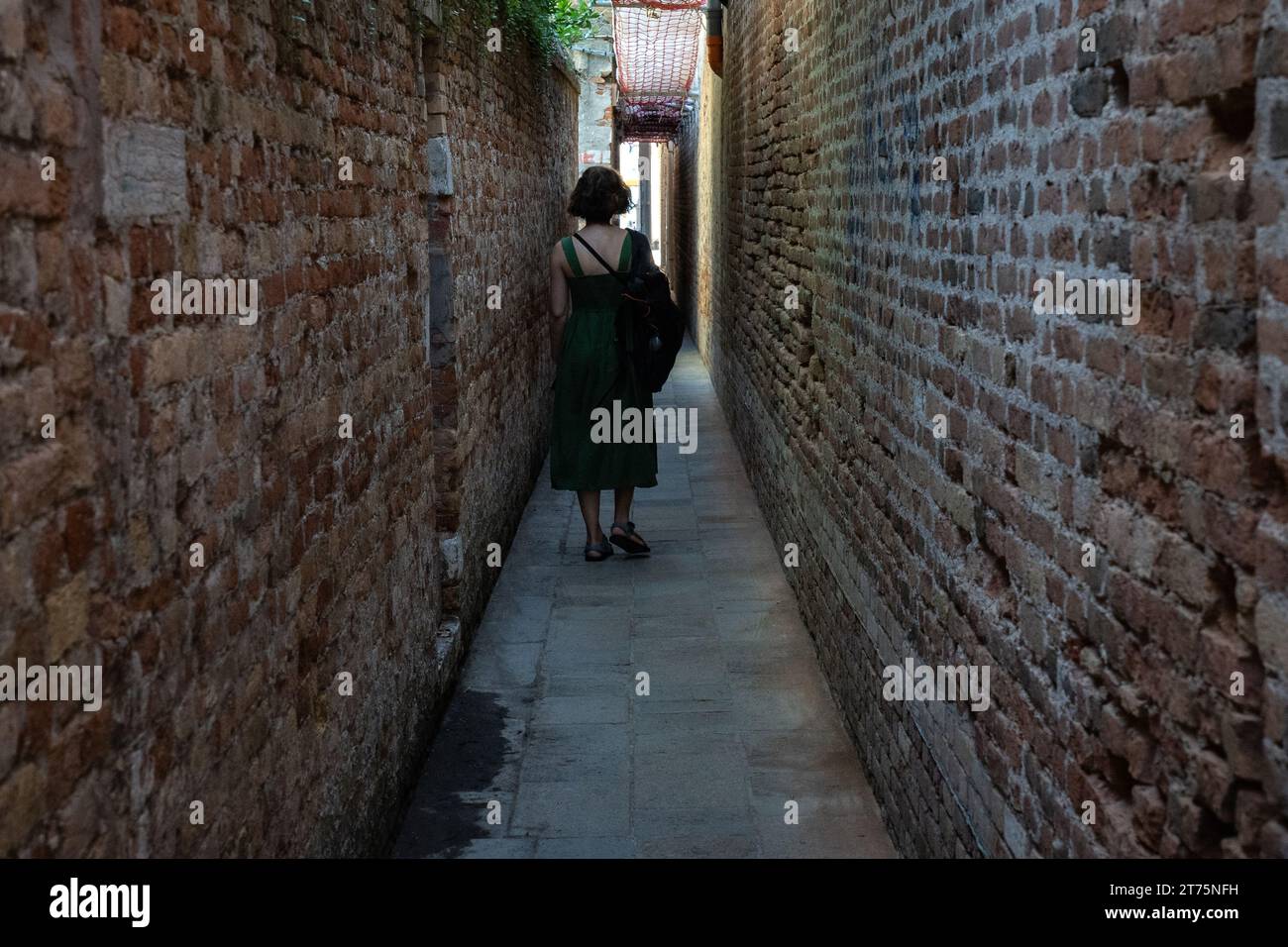 Back of a woman walking in a narrow alley between two brick wall ...