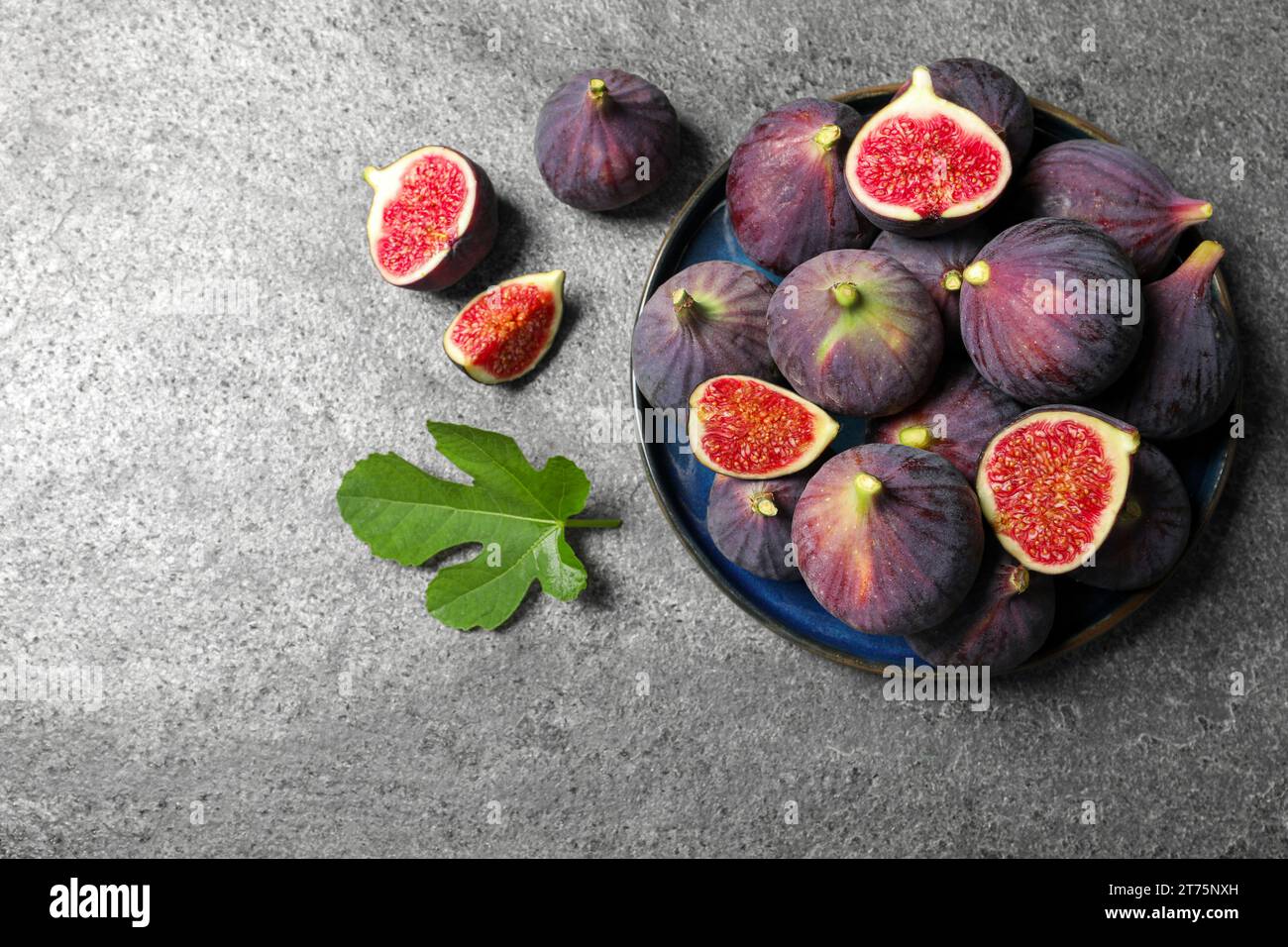 Whole and cut ripe figs with leaf on light grey textured table, flat ...