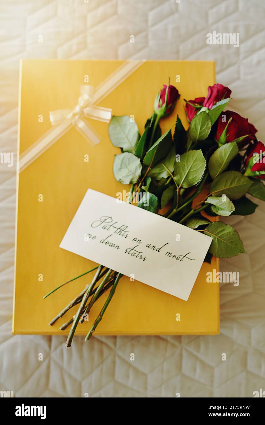 Box, roses and letter on bed, gift and invitation in closeup, above or ...