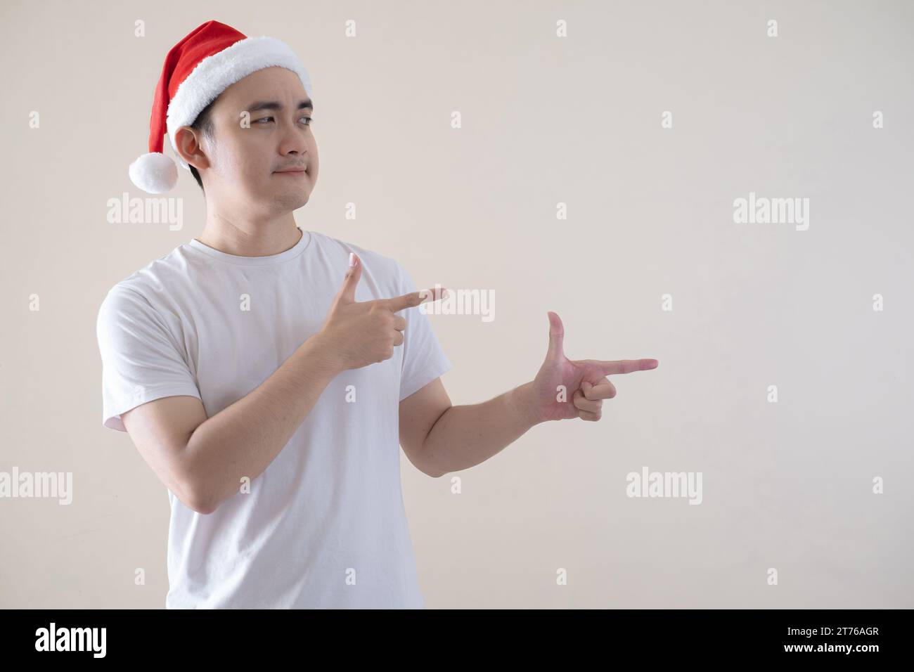 Young Asian Santa man is pointing to the right side on isolated beige ...