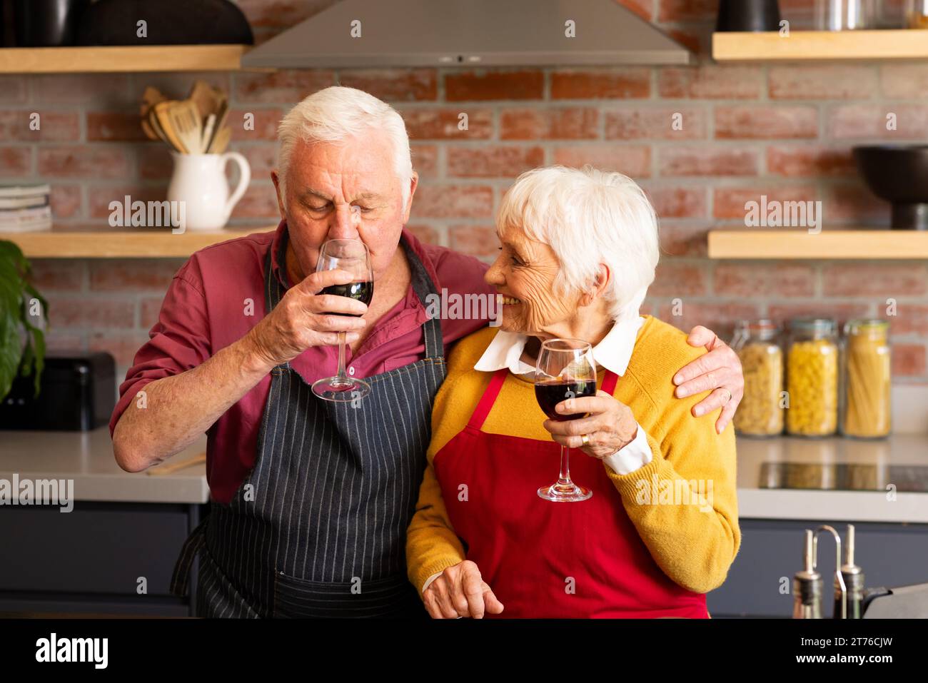Happy caucasian senior couple cooking, drinking wine and embracing in ...