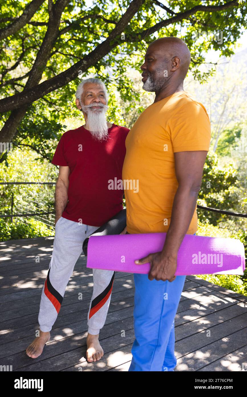 Two happy diverse male senior friends with mats talking before yoga ...