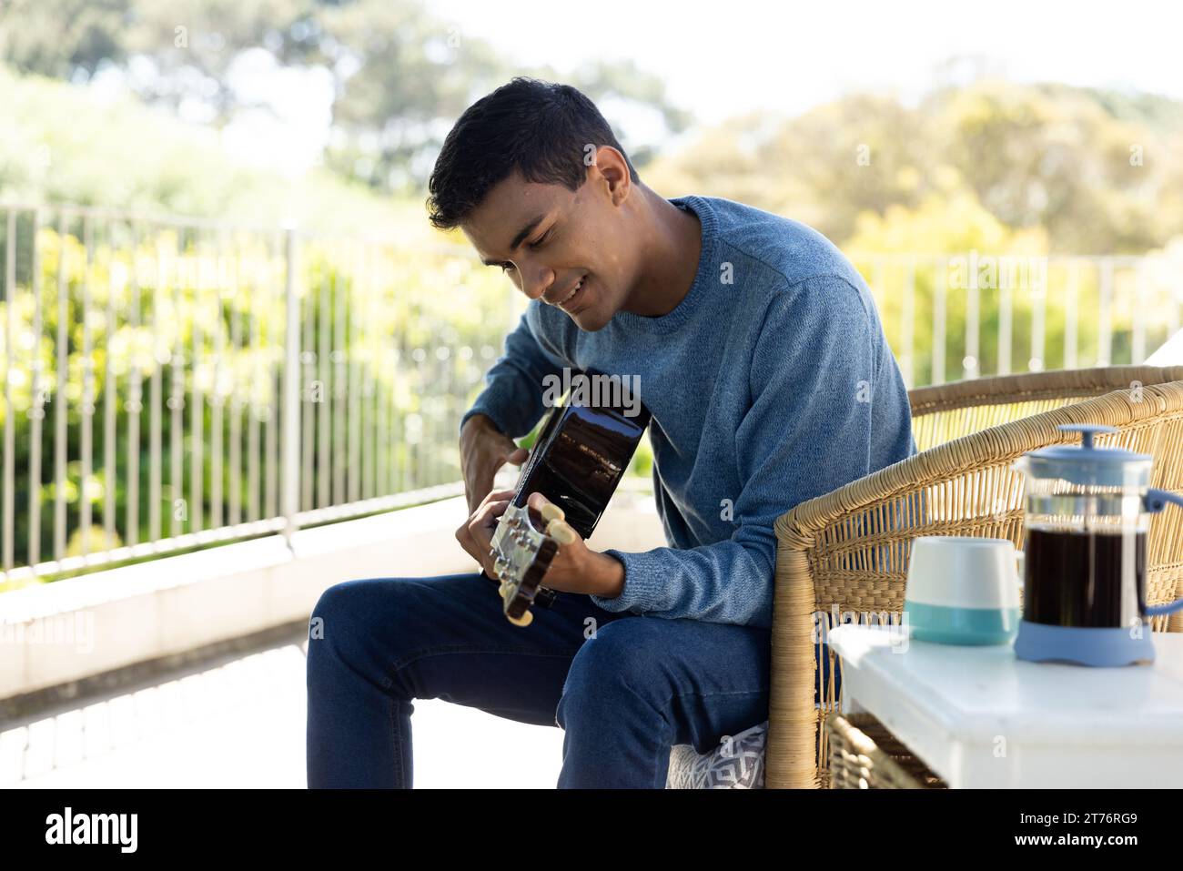 Happy biracial man sitting on balcony playing guitar at home Stock Photo - Alamy