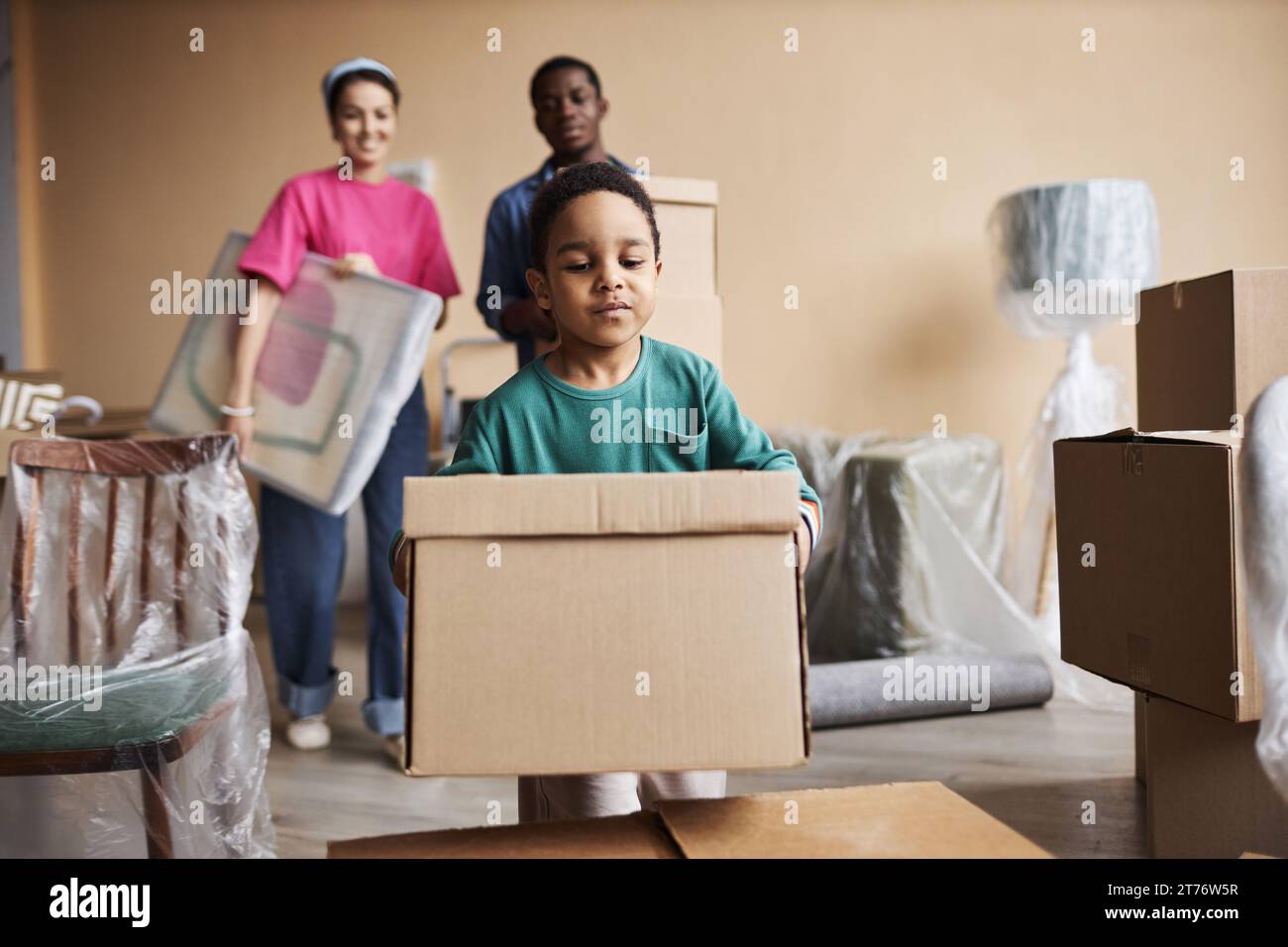 Cute little boy carrying packed cardboard box and putting it on top of ...
