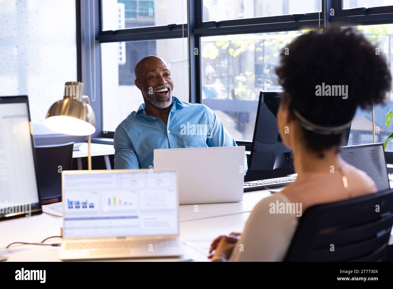 Happy diverse female and male colleague using laptops, talking across ...