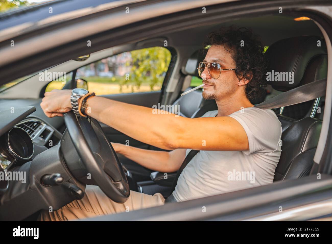 Handsome man with curly hair and sunglasses, drives a car and smokes a ...
