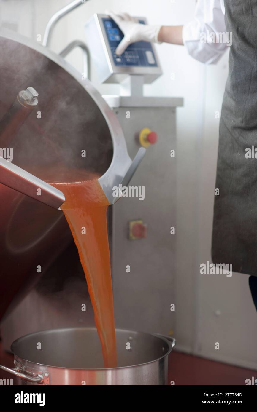 Factory worker using computer controlled machinery pouring tomato sauce ...