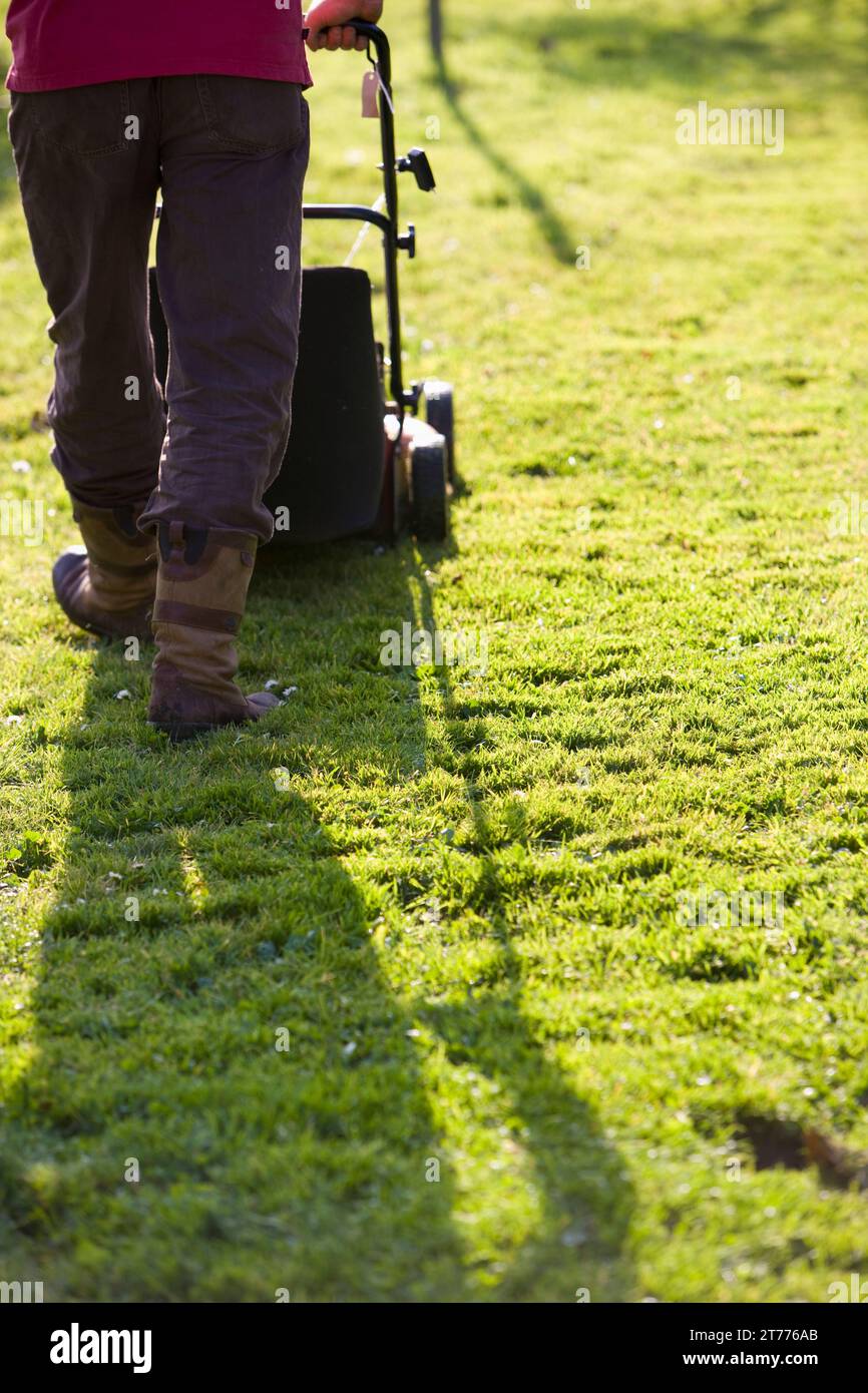 Back view of a gardener pushing a lawnmower Stock Photo - Alamy