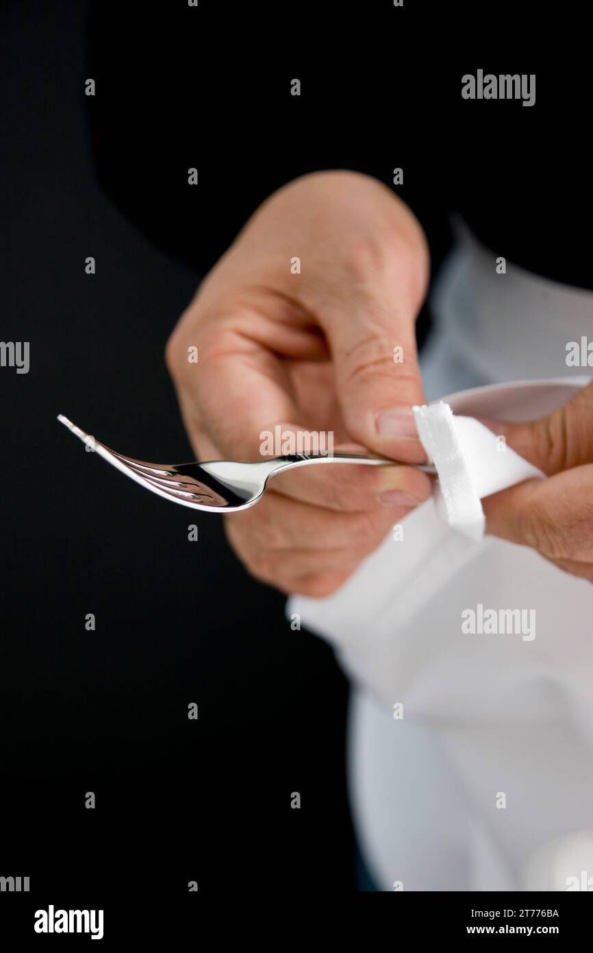 Close up of a waiter hands polishing a silver fork with a white napkin ...