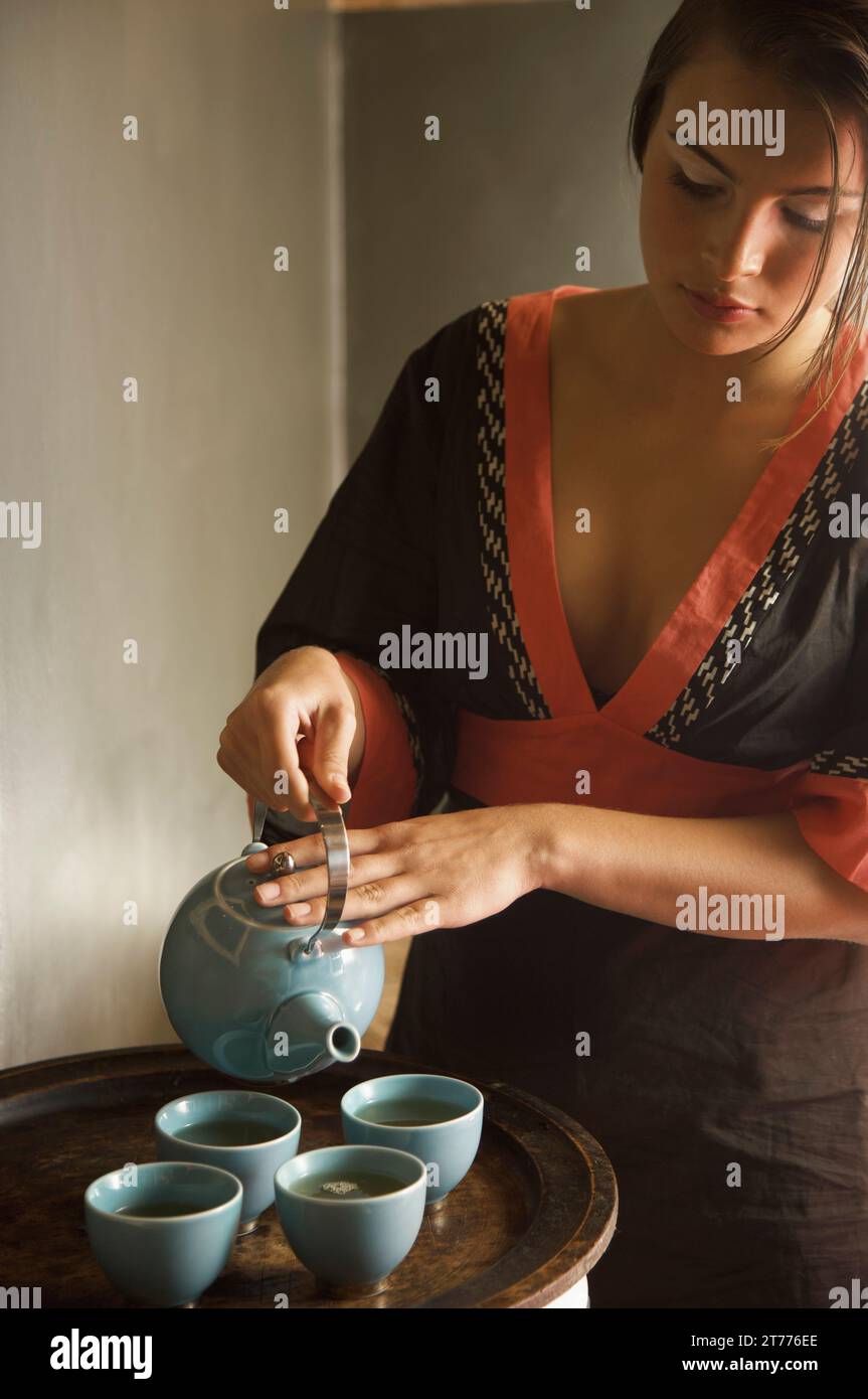 Young woman holding teapot and pouring green tea Stock Photo - Alamy