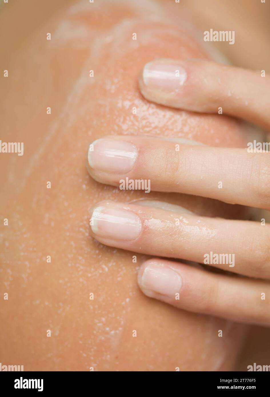 Extreme close up of a woman hand rubbing shower gel on her shoulder ...