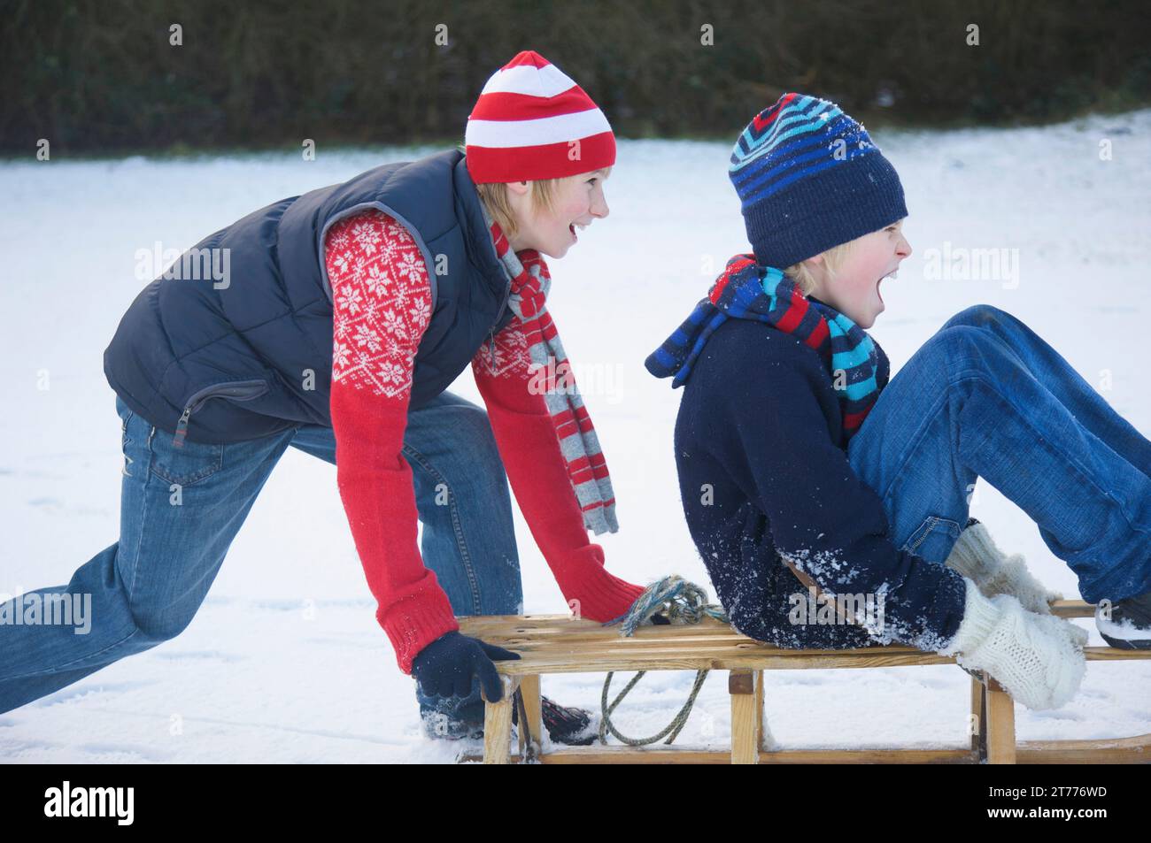 Profile of a boy pushing a friend sitting on a sled Stock Photo - Alamy