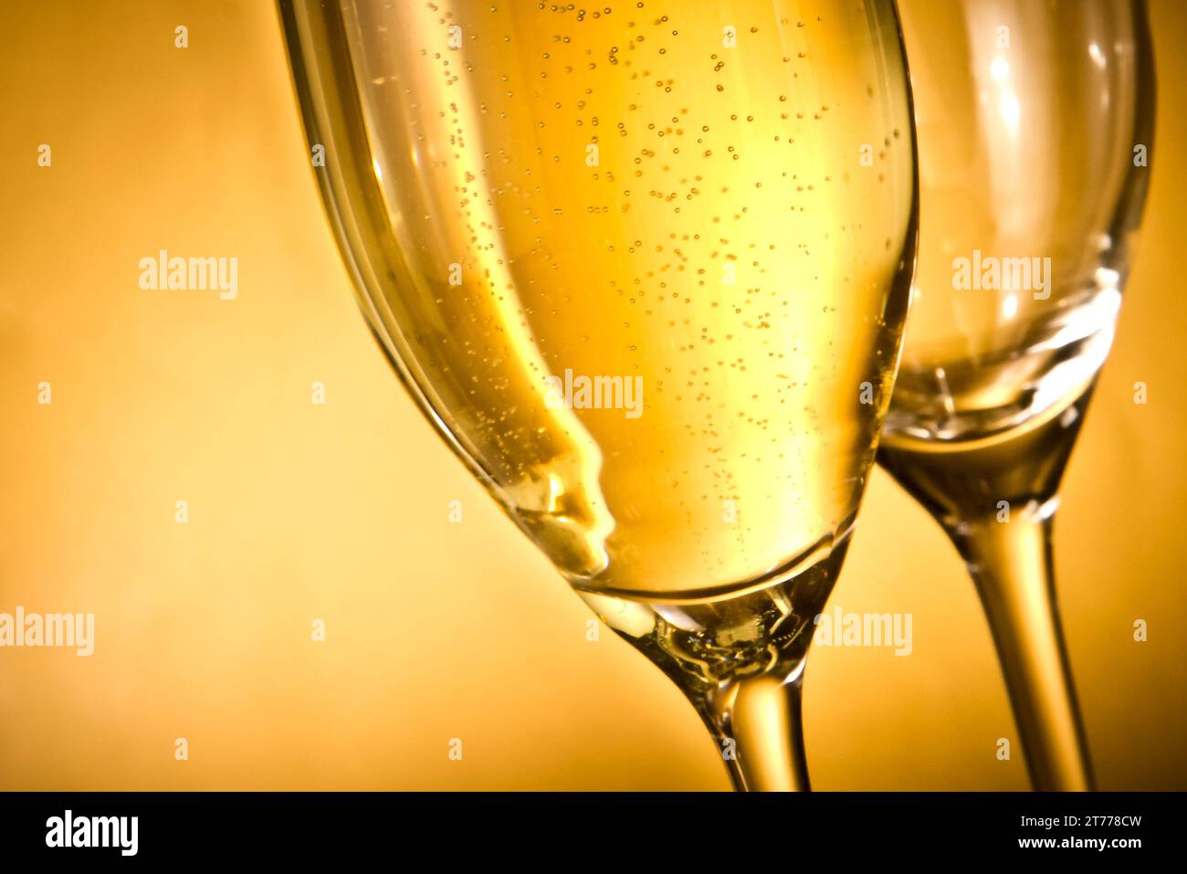 one flute of champagne and one empty with golden bubbles against golden ...