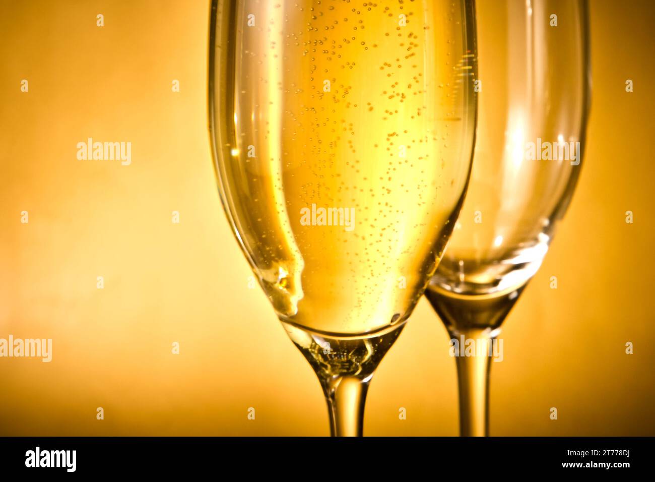 one glass of champagne and one empty with golden bubbles against golden ...