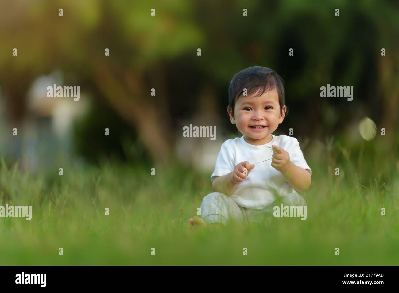happy infant baby sitting on a green grass field at the park Stock ...