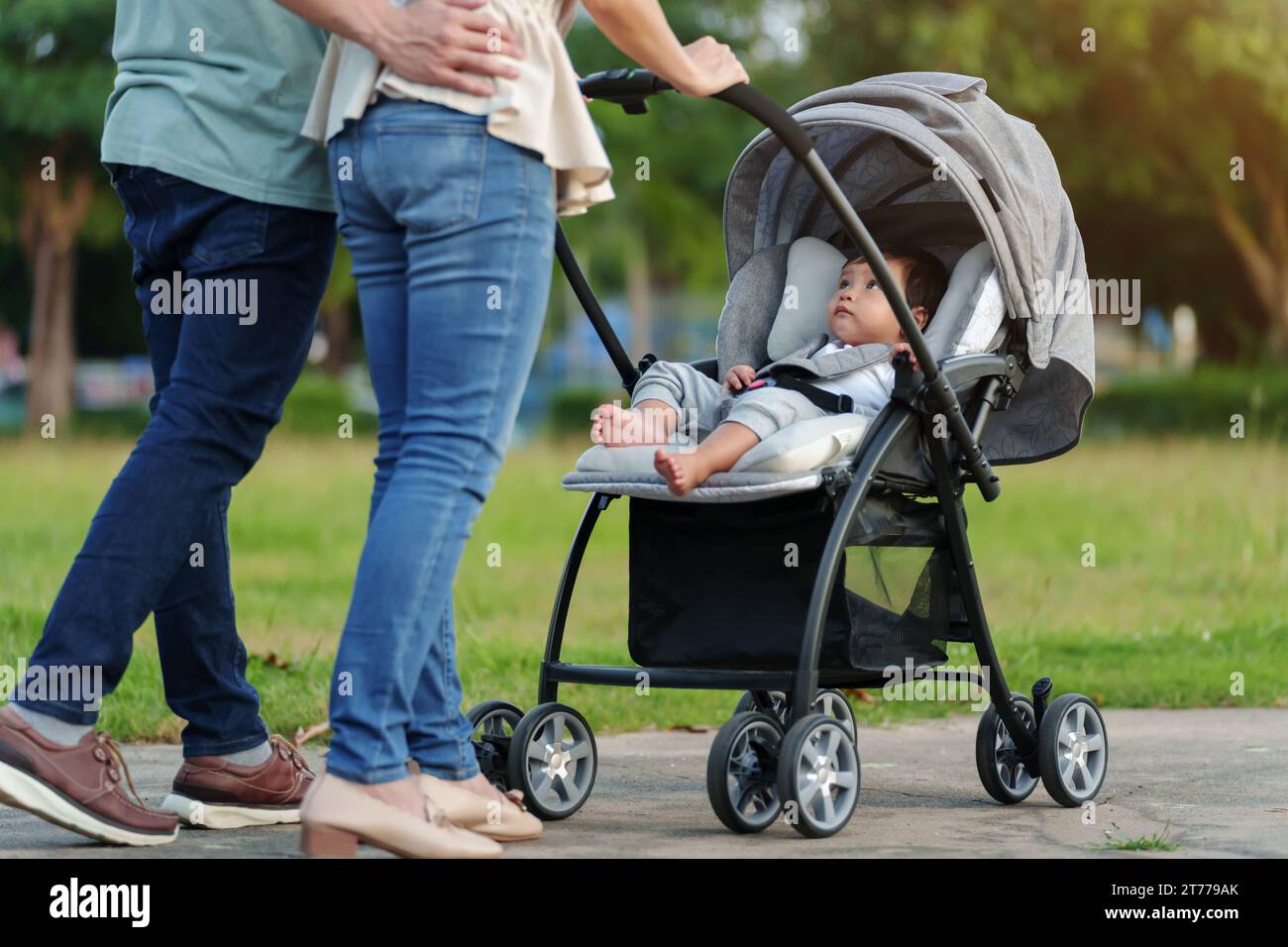 parent (father and mother) pushing infant baby stroller and walking in ...