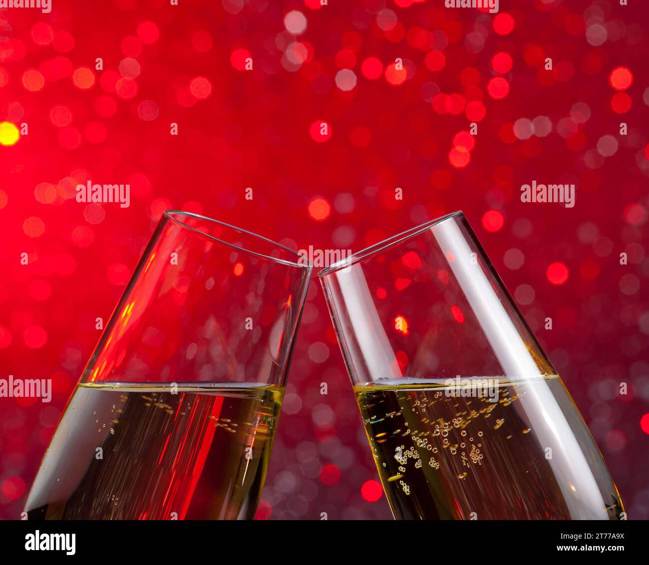 pair of champagne flutes with gold bubbles make cheers on red light ...