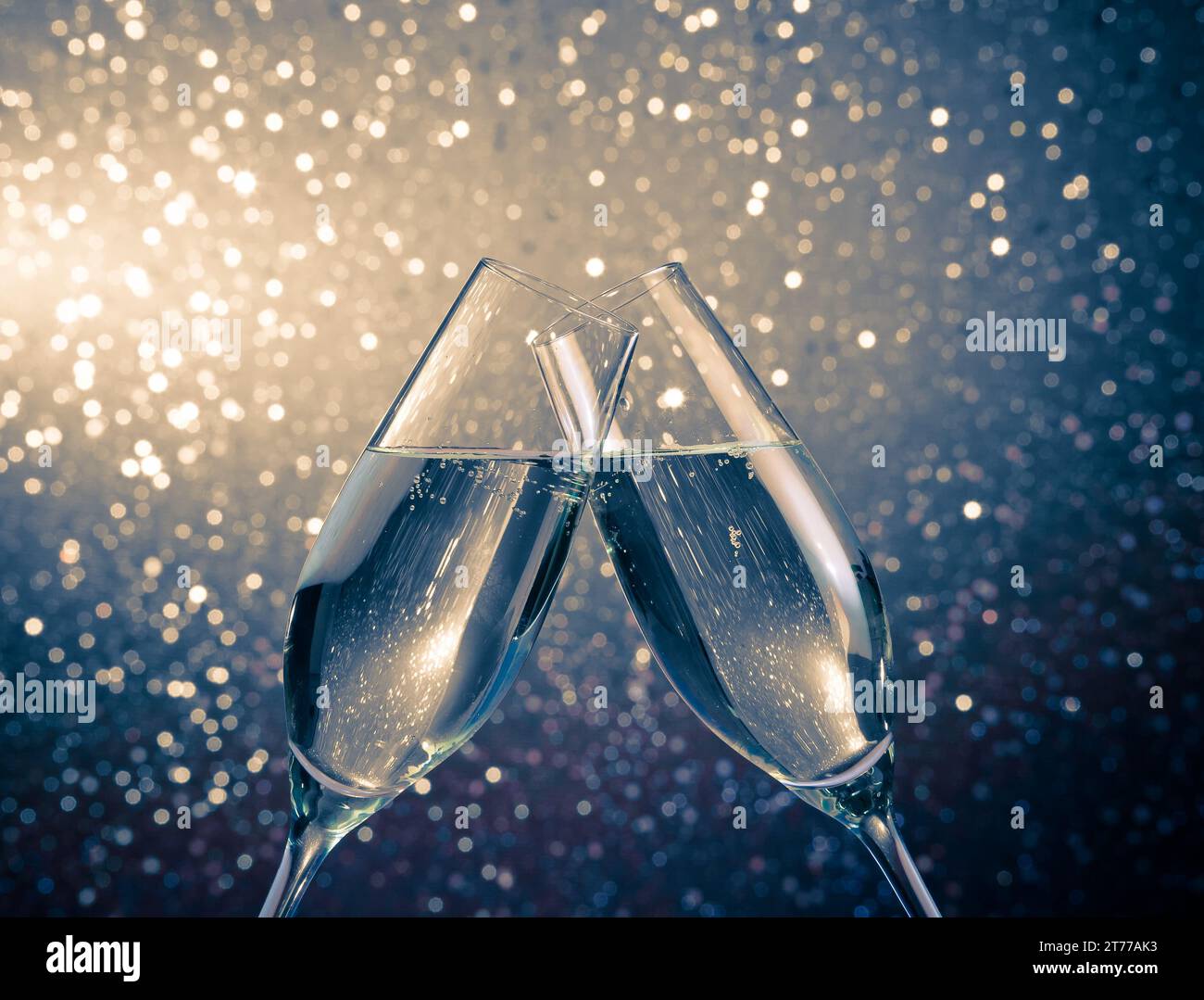 two champagne flutes with golden bubbles make cheers on blue light ...