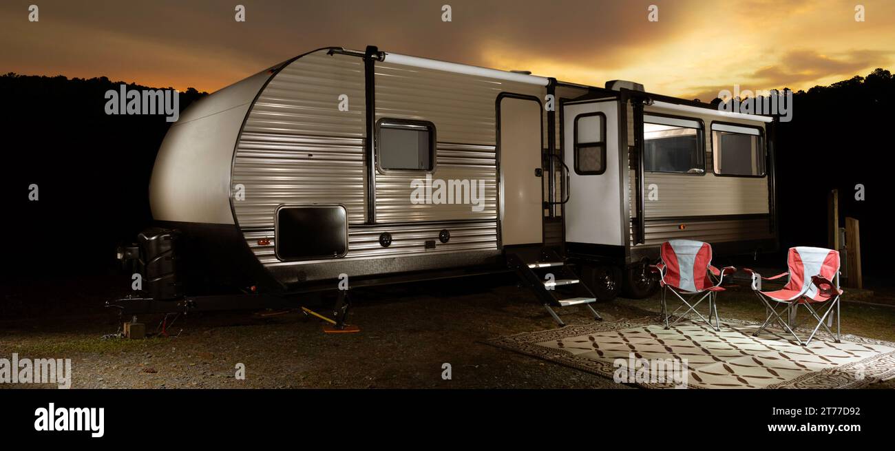 Travel trailer with a colorful sunset going down behind a tree covered ...