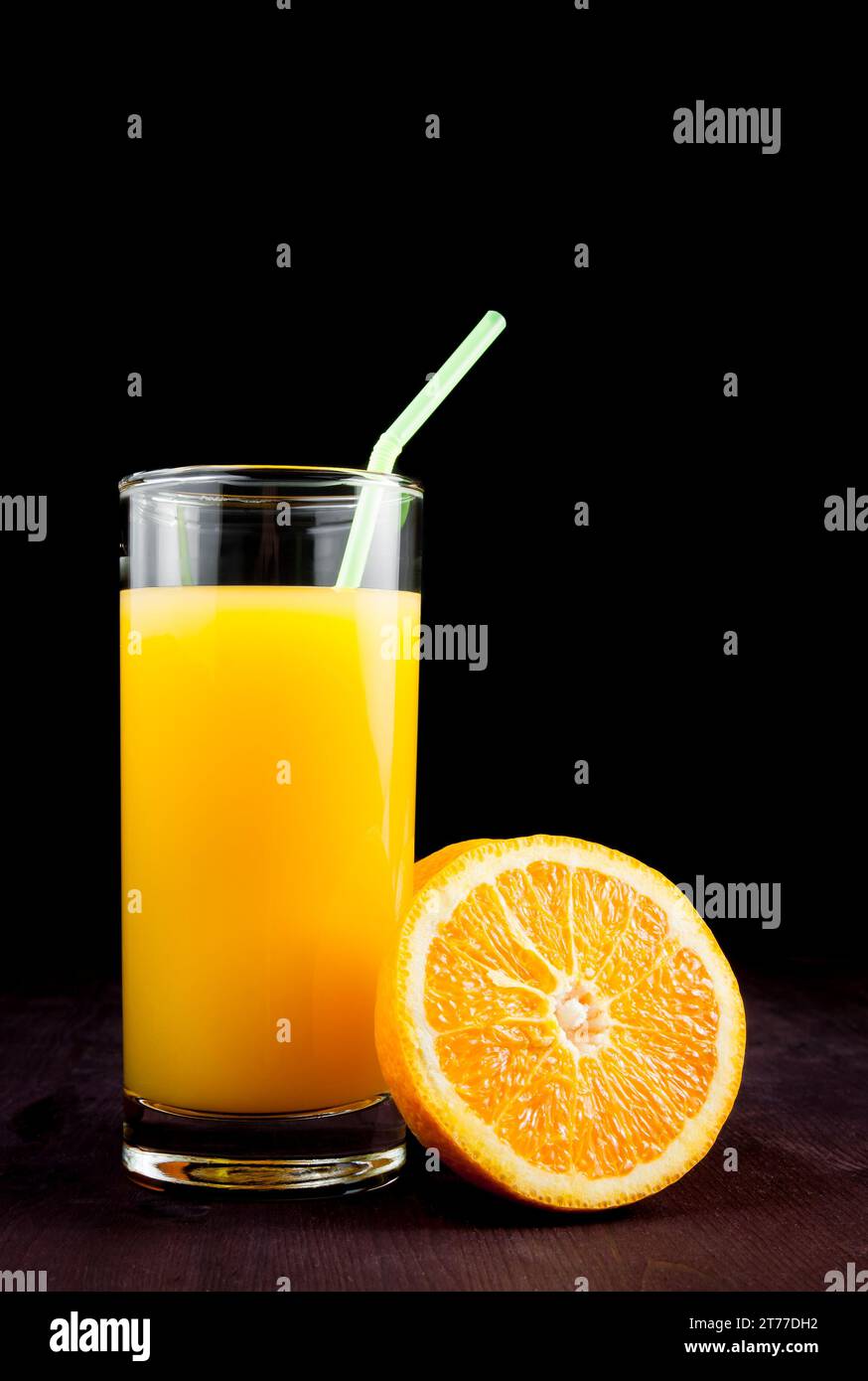 full glass of orange juice with straw near half orange on black ...