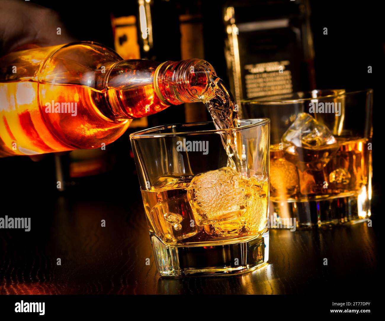 barman pouring whiskey in front of whiskey glass and bottles on wood ...