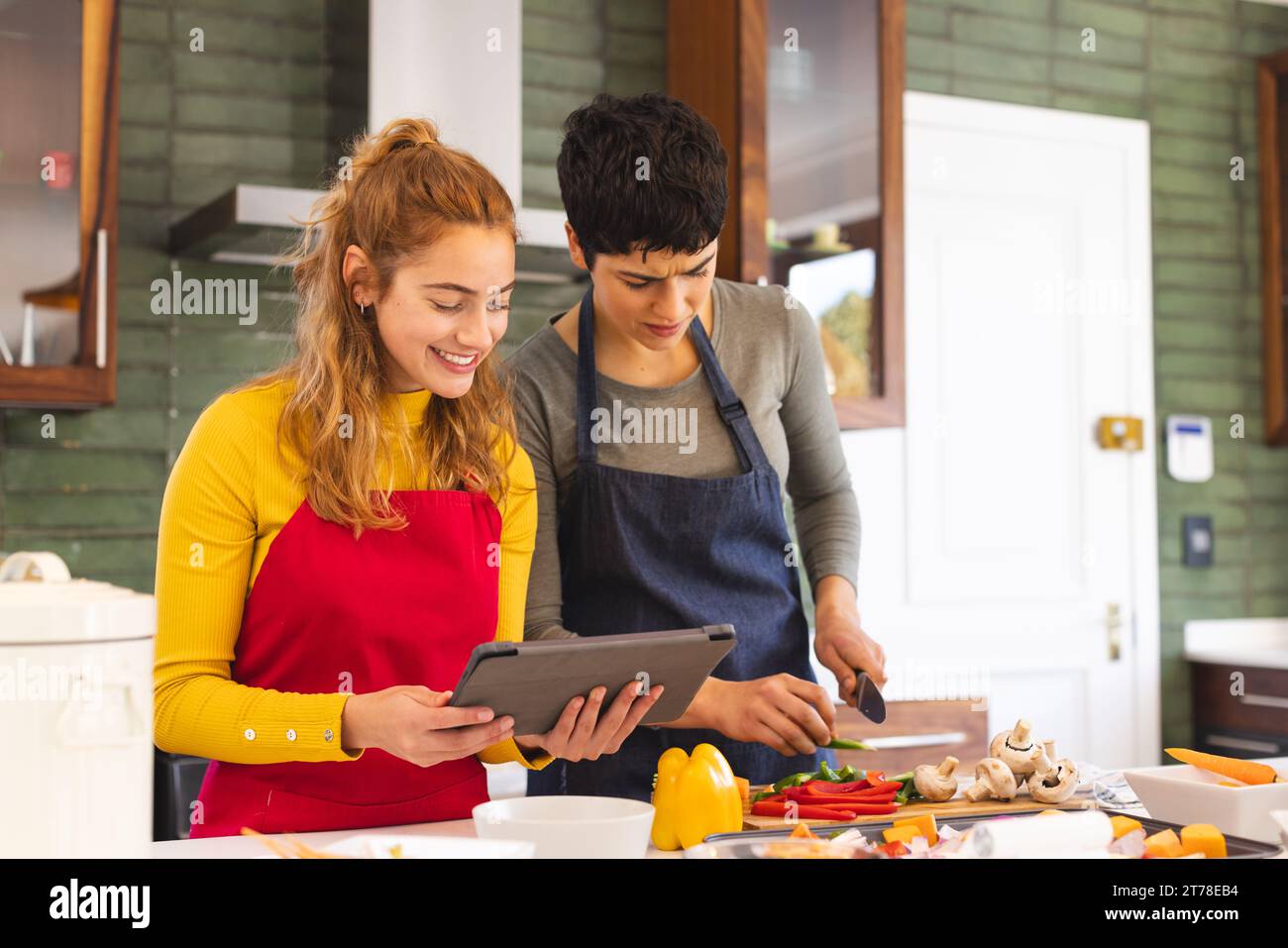 Happy biracial lesbian couple using tablet preparing vegetables in ...