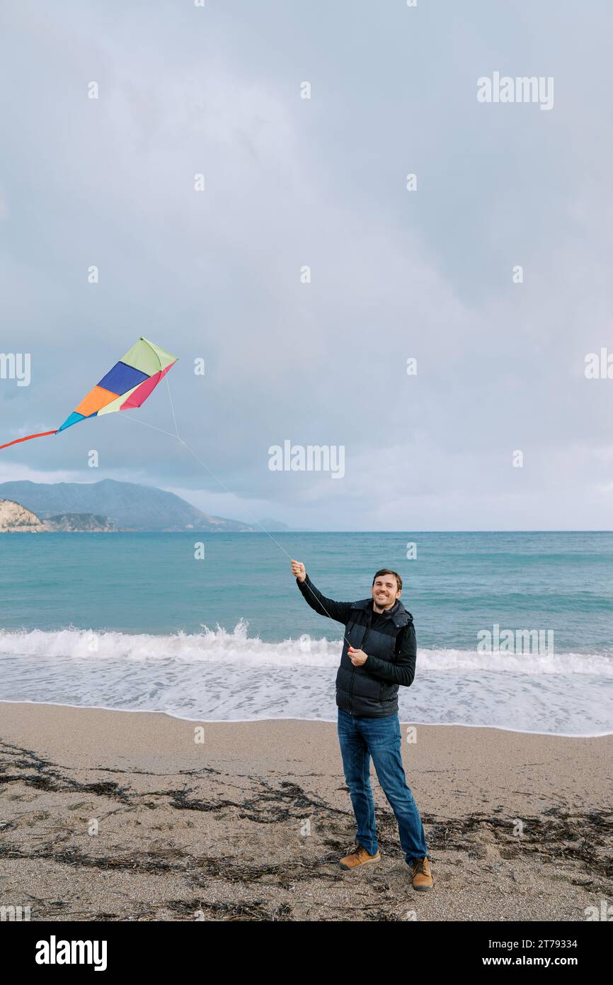Young smiling man flying a colorful kite on a rope on the beach Stock ...