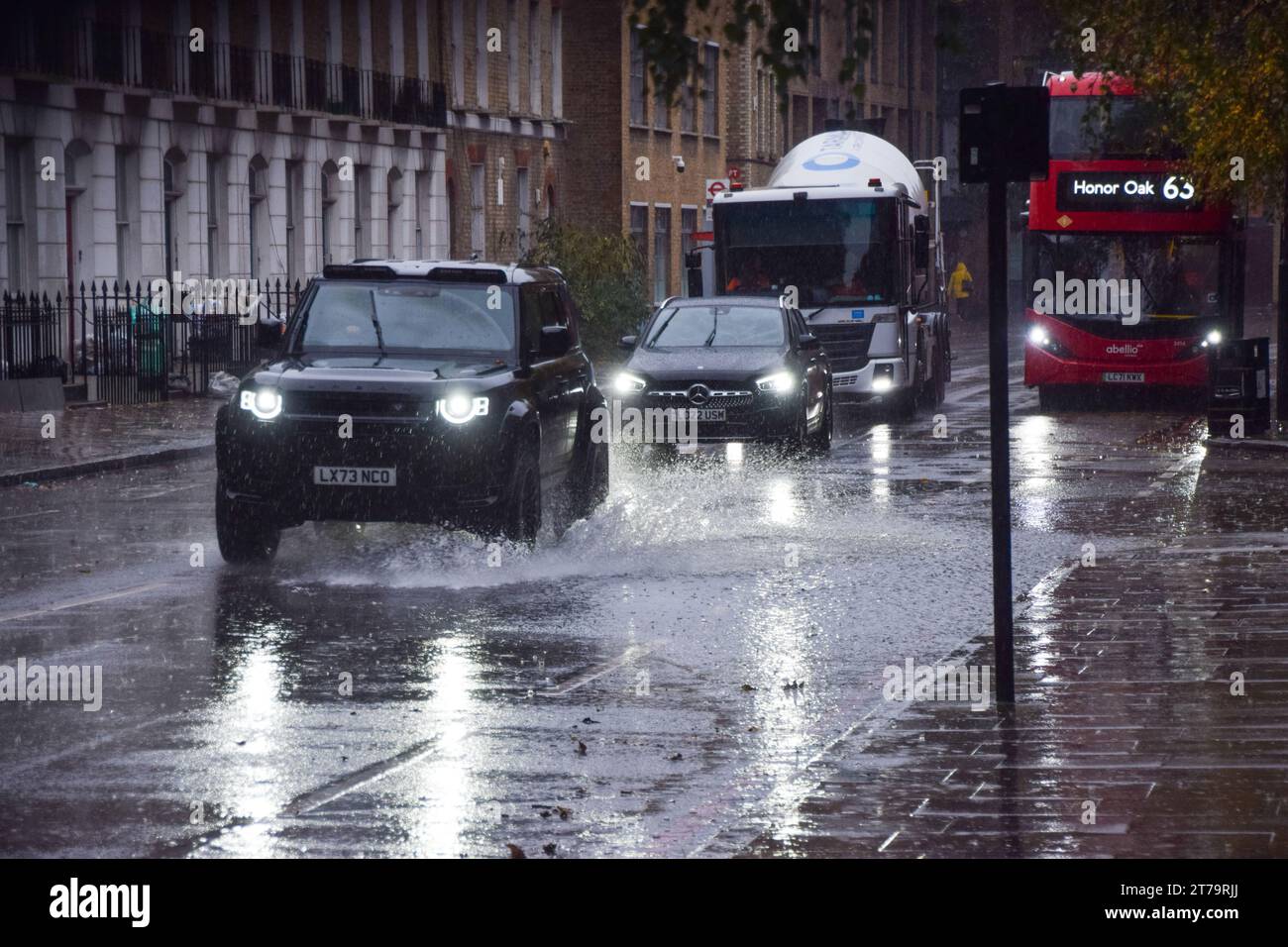 London, UK. 14th November 2023. Cars drive through a large puddle in ...