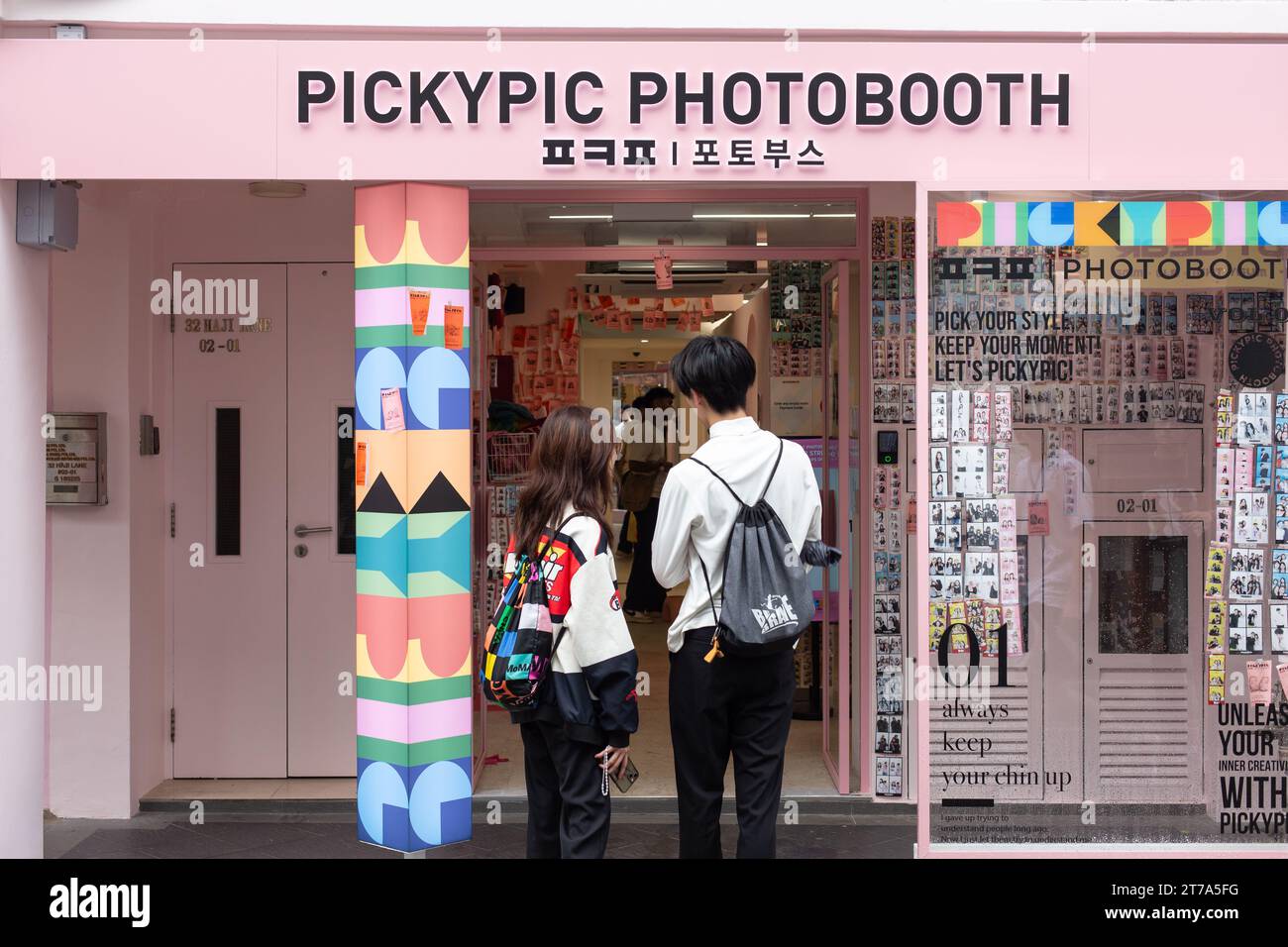 A tennage boy and girl outside are checking out the pink colour photo booth shop at Haji Lane ...